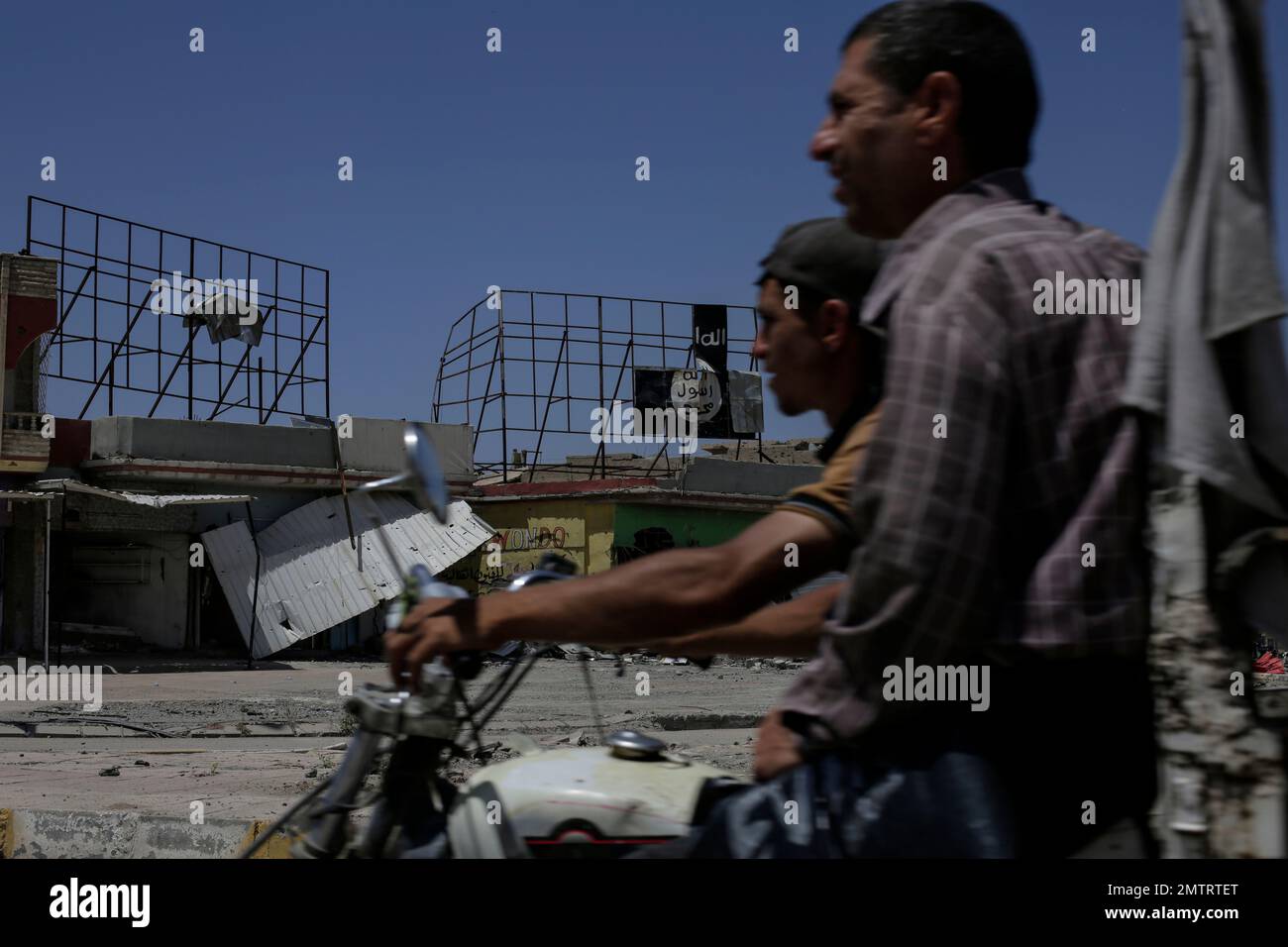 Two men carrying a white flag on their motorbike pass an Islamic State ...
