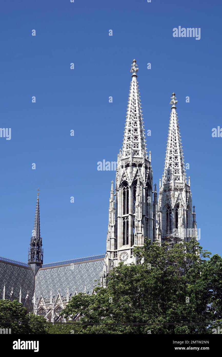 Two high spires on Votivkirche and church roof rise above green tree ...