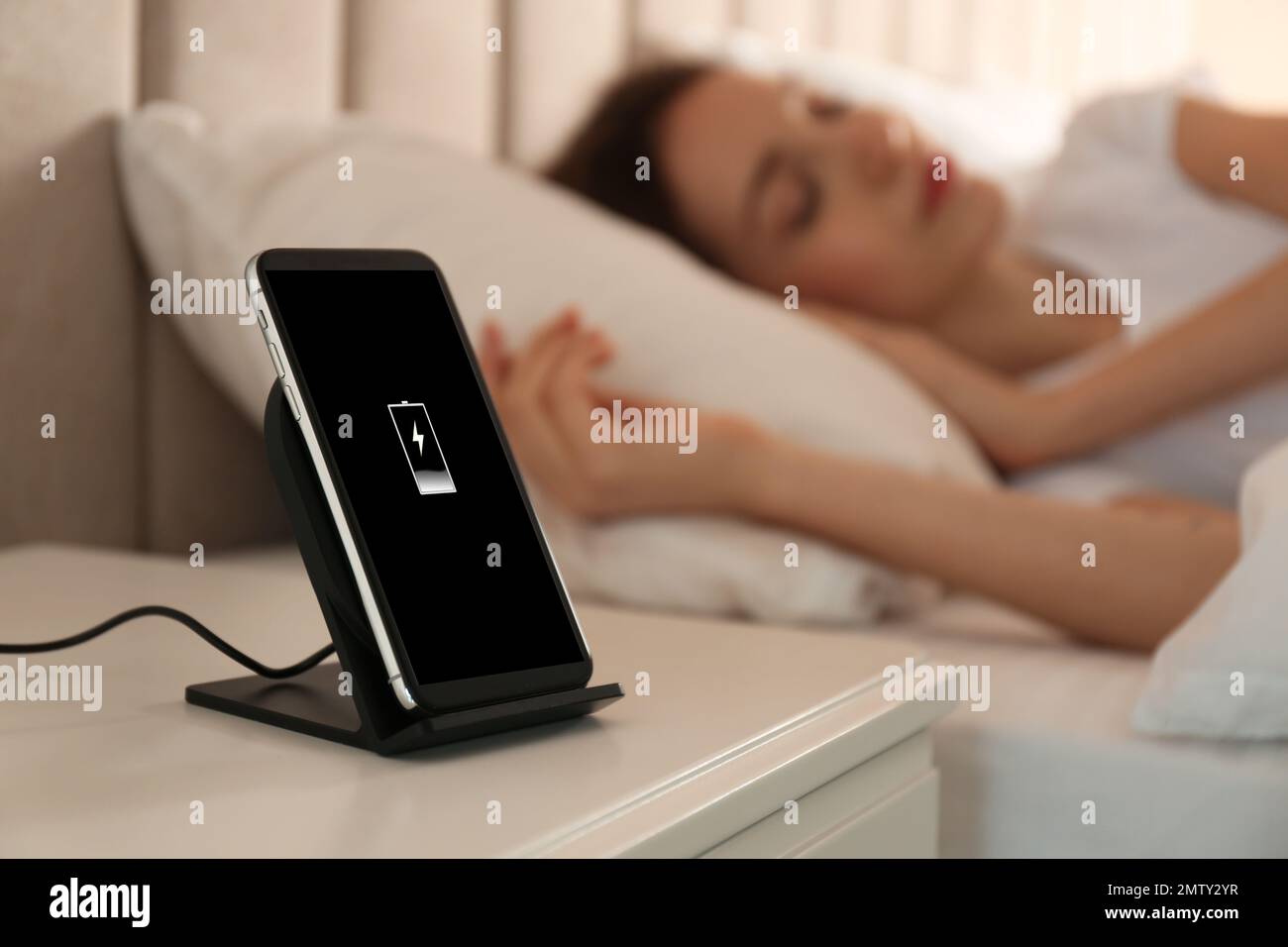Smartphone charging on wireless pad and woman sleeping in bed Stock ...
