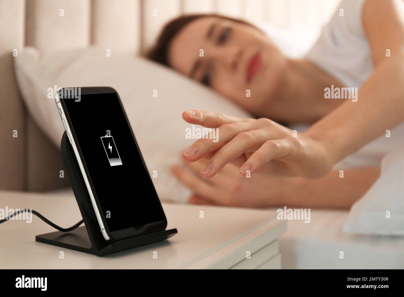 Woman taking smartphone from wireless charger in bedroom Stock Photo ...