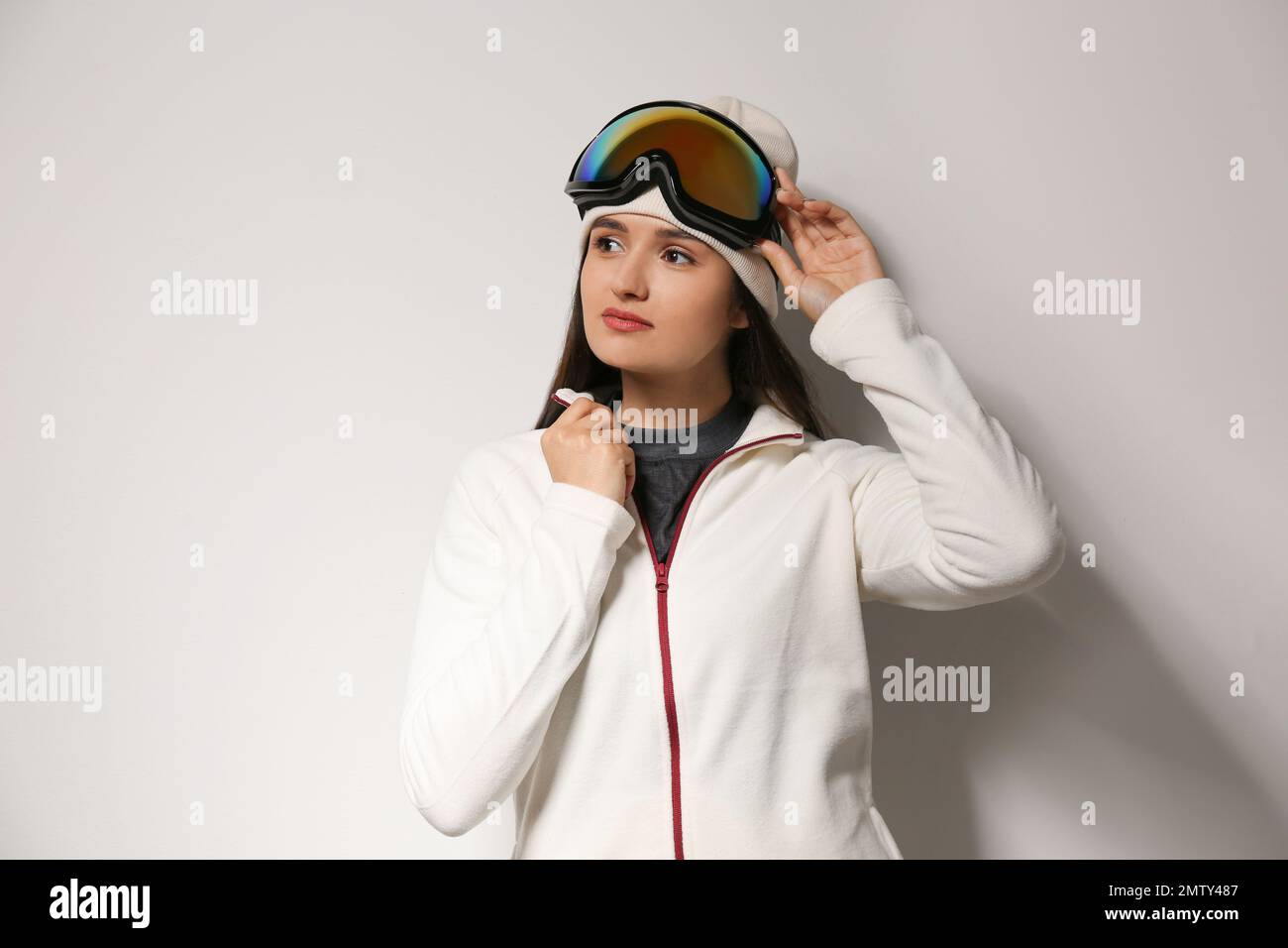 Woman wearing fleece jacket and goggles on light grey background ...