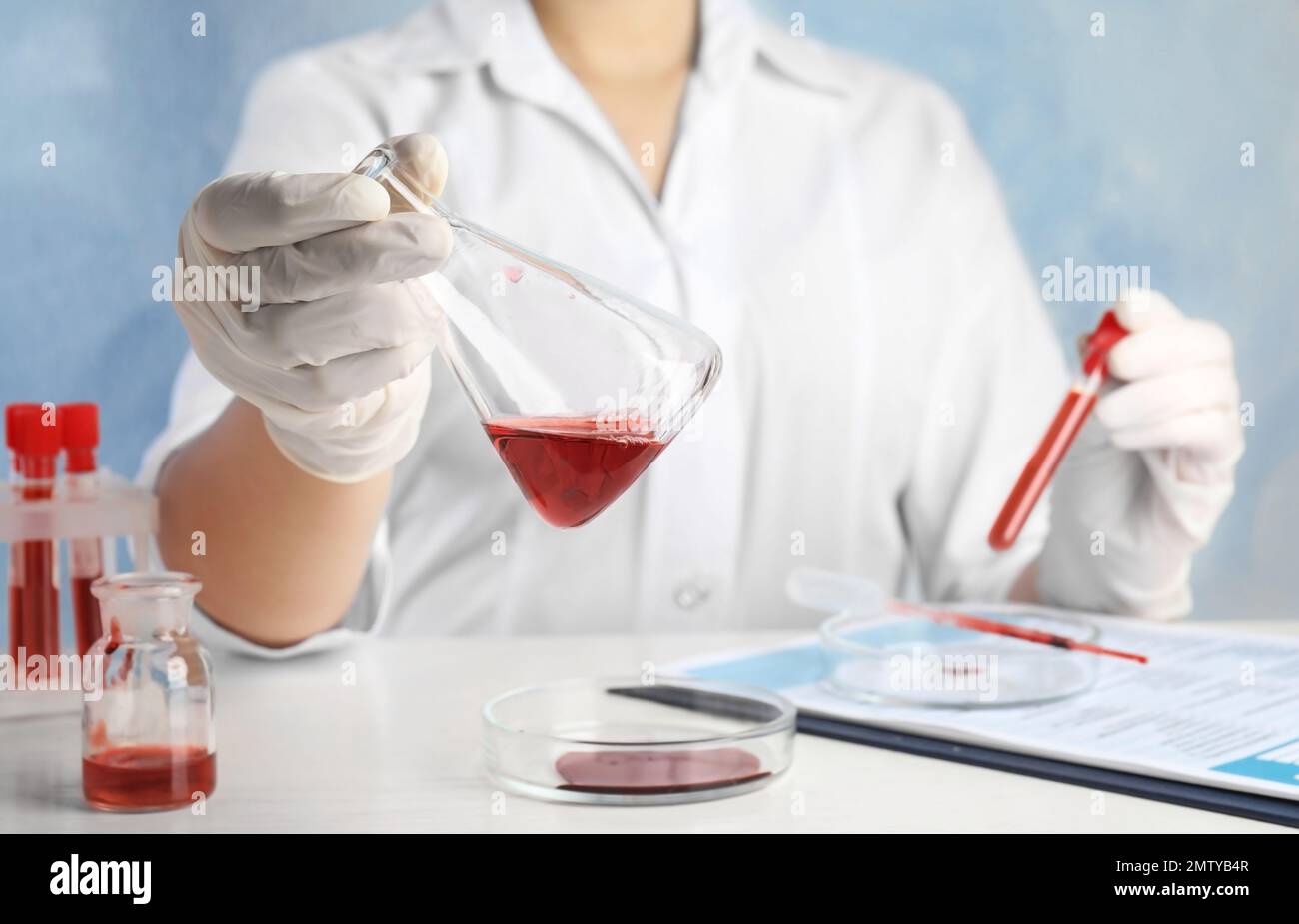 Scientist holding conical flask and tube with blood samples at table ...