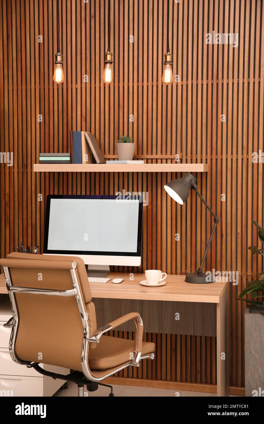 Comfortable workplace with computer near wooden wall in stylish room ...
