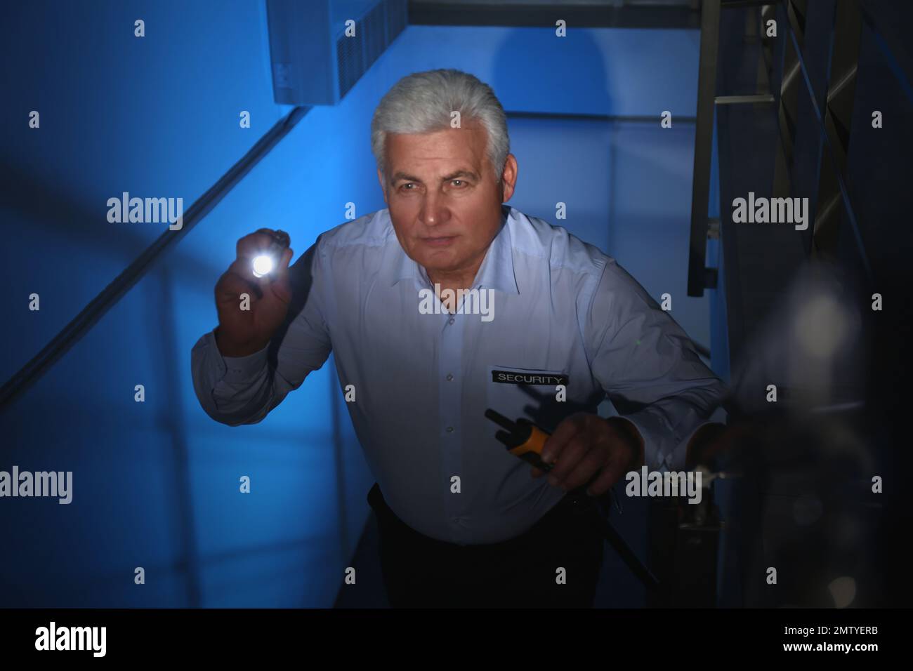 Professional security guard with flashlight on stairs in dark room ...