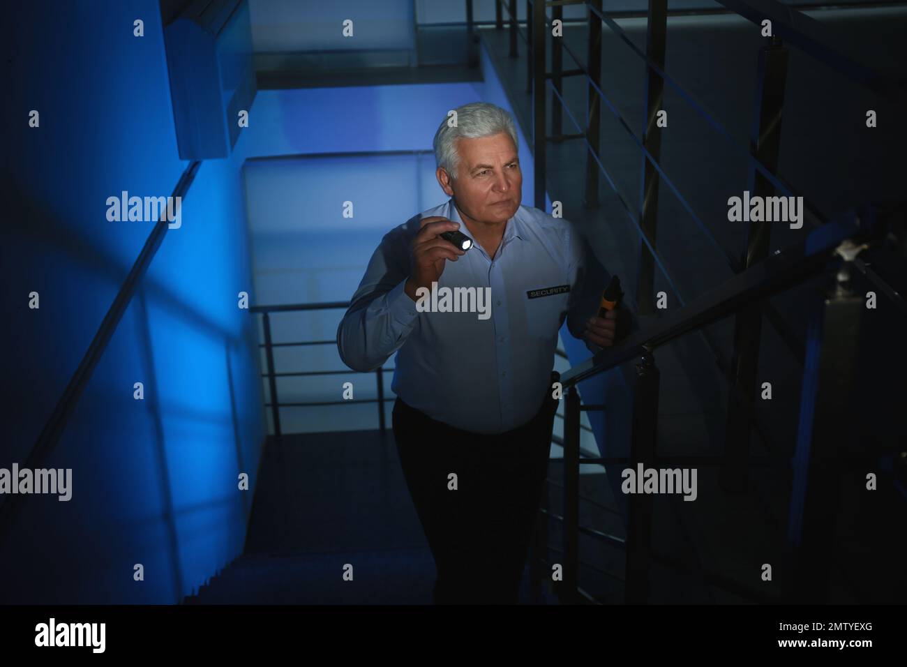 Professional security guard with flashlight on stairs in dark room ...