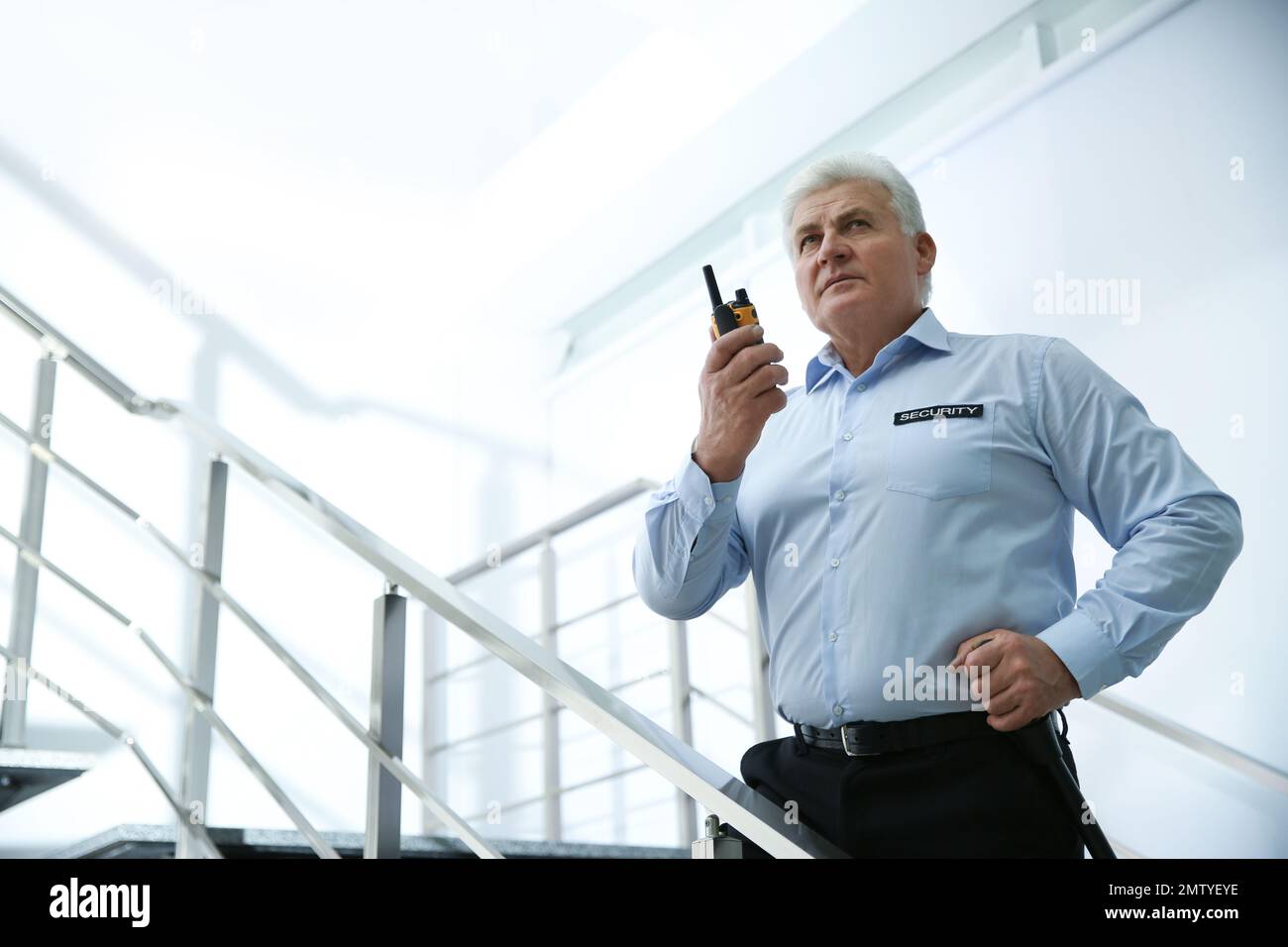 Professional security guard with portable radio set on stairs indoors ...