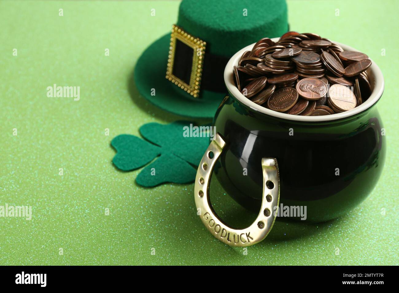 Pot of gold coins, horseshoe, hat and clover on green background, space ...