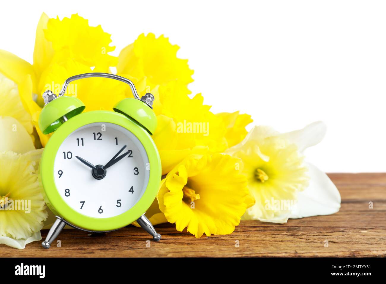 Green alarm clock and spring flowers on wooden table against white ...