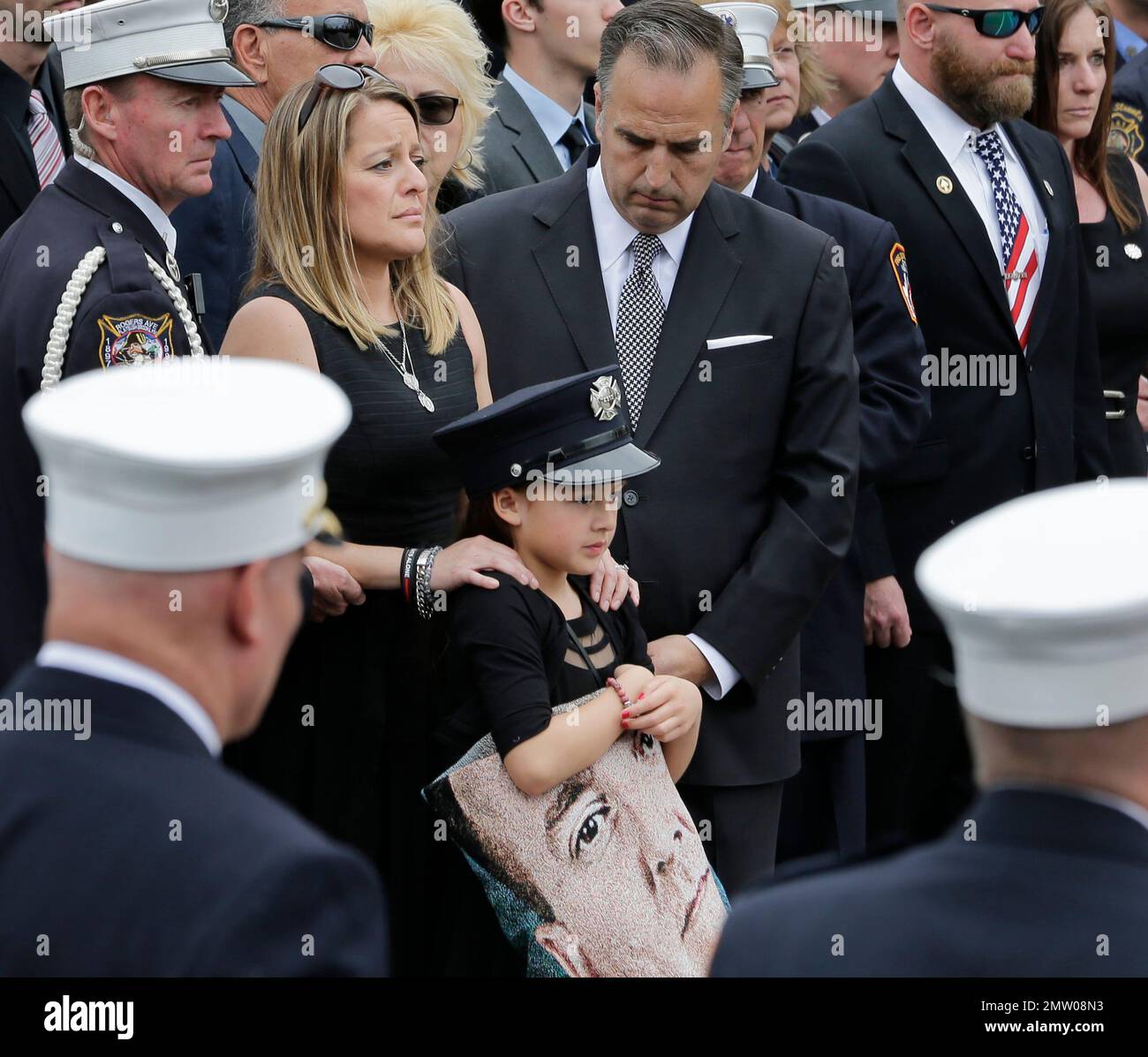 While Isabella Tolley, 8, center, holds a blanket with a picture of her ...