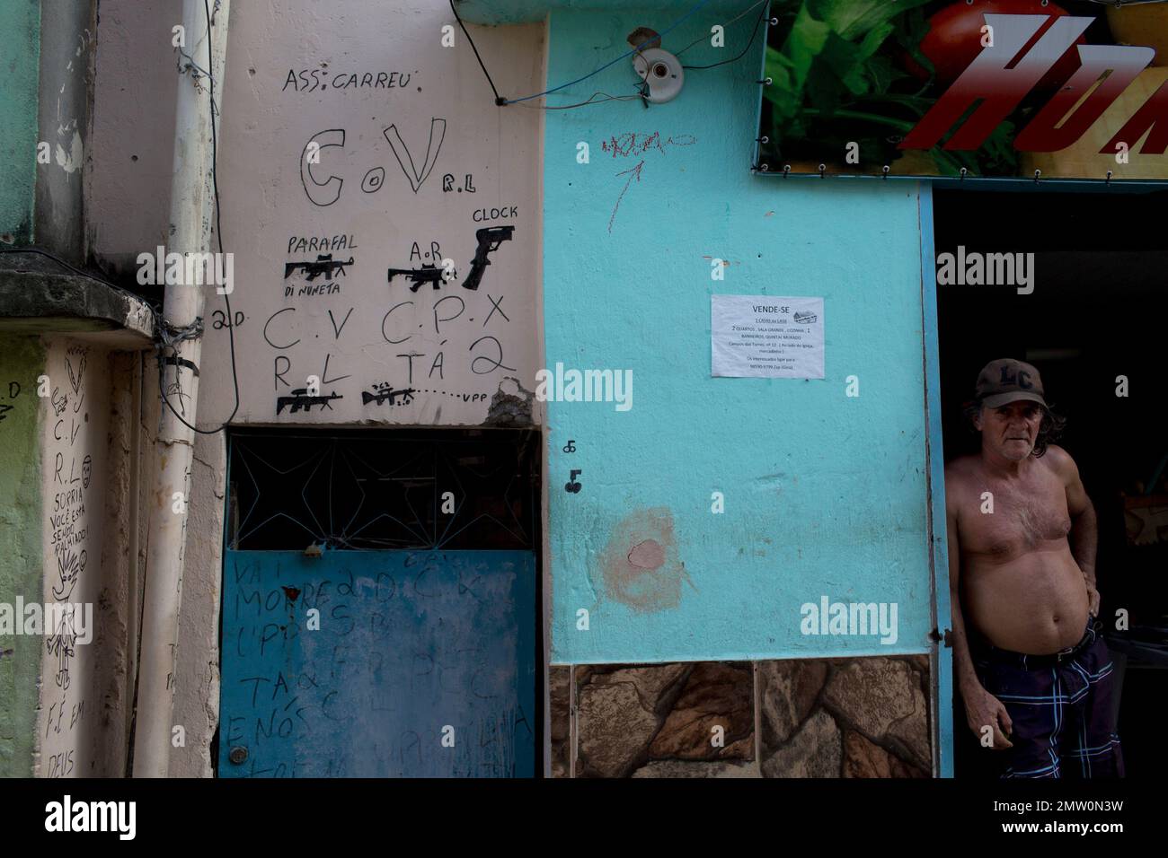 A man stands next to a wall covered with hand drawn signs by drug gangs ...