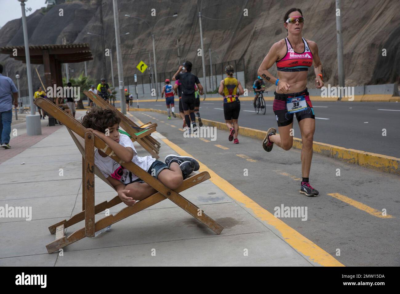 A boy rests on a beach chair as a competitor runs by during a half Iron ...