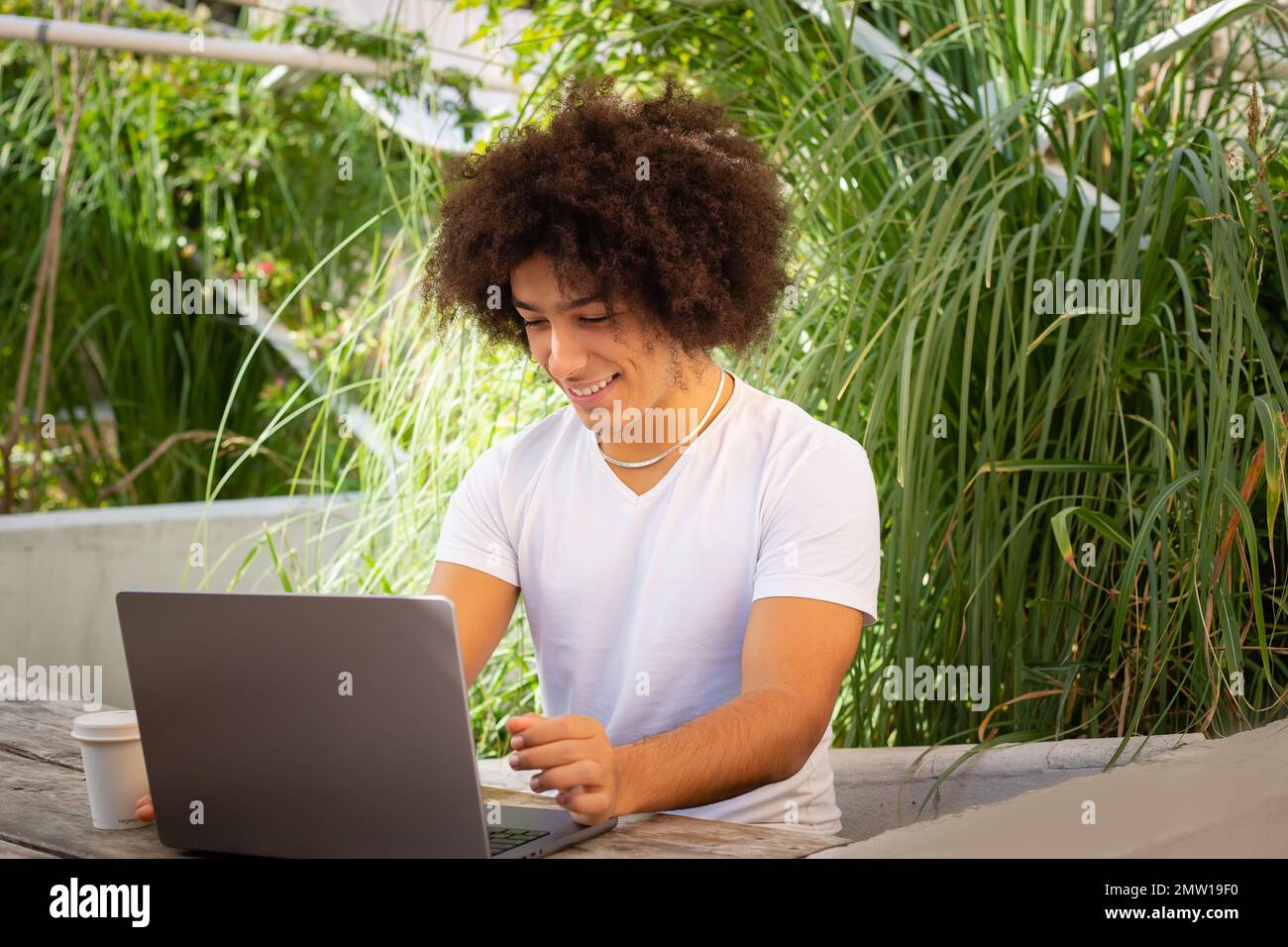 Smiling young ethnic man african-italian works on a laptop outdoors, in ...