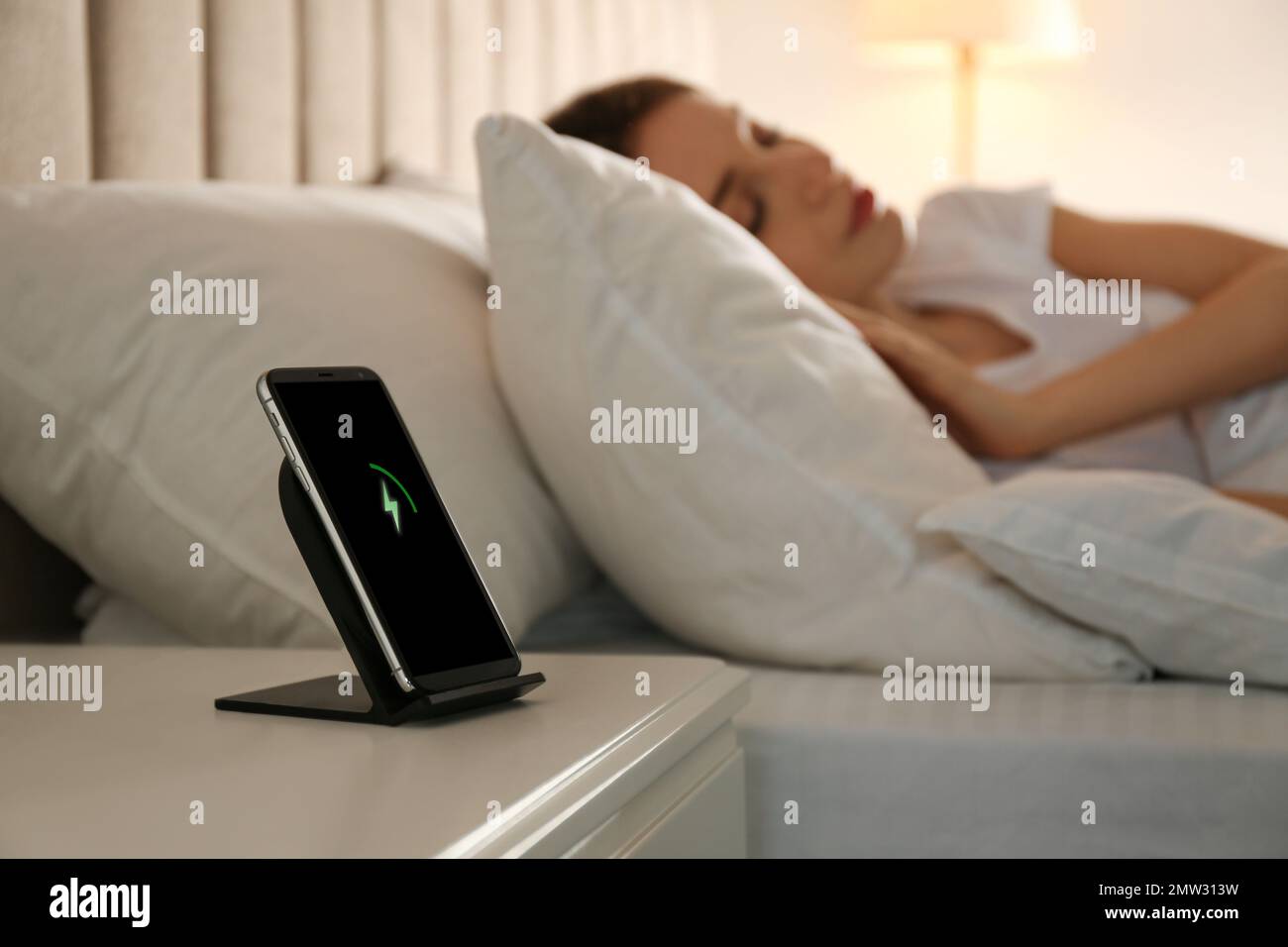 Smartphone charging on wireless pad and woman sleeping in bed Stock Photo - Alamy