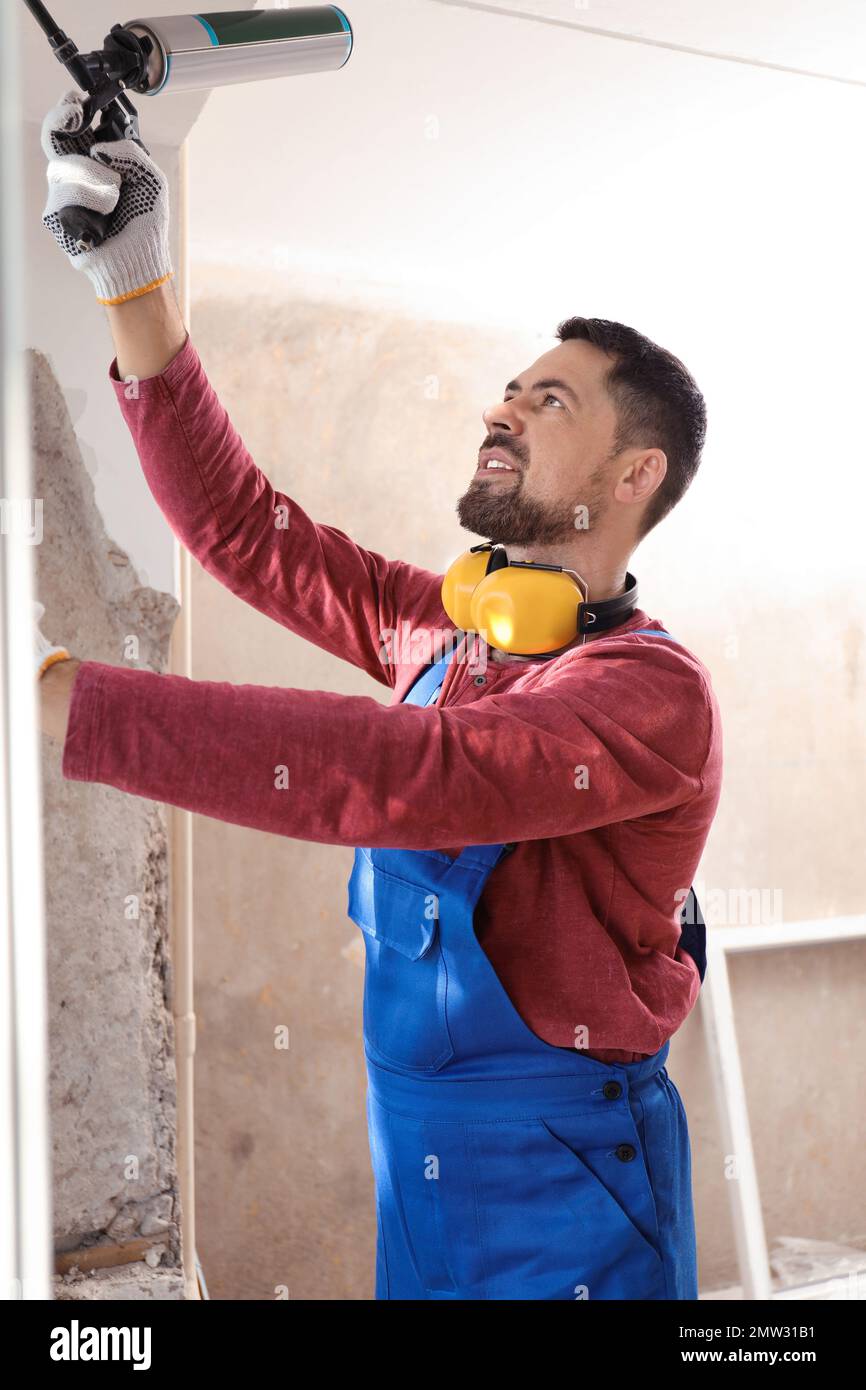Worker using foam gun for window installation indoors Stock Photo - Alamy
