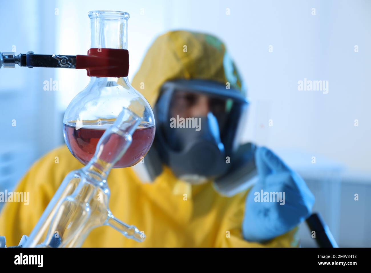 Flask with reagent and scientist in chemical protective suit working at ...