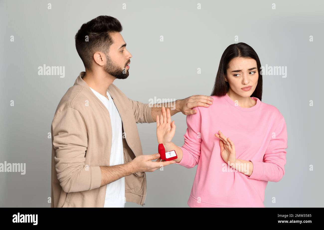 Young woman rejecting engagement ring from boyfriend on light grey ...