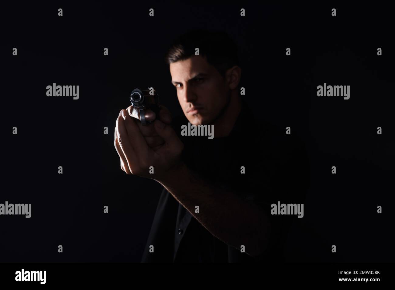 Professional killer with gun on black background Stock Photo - Alamy