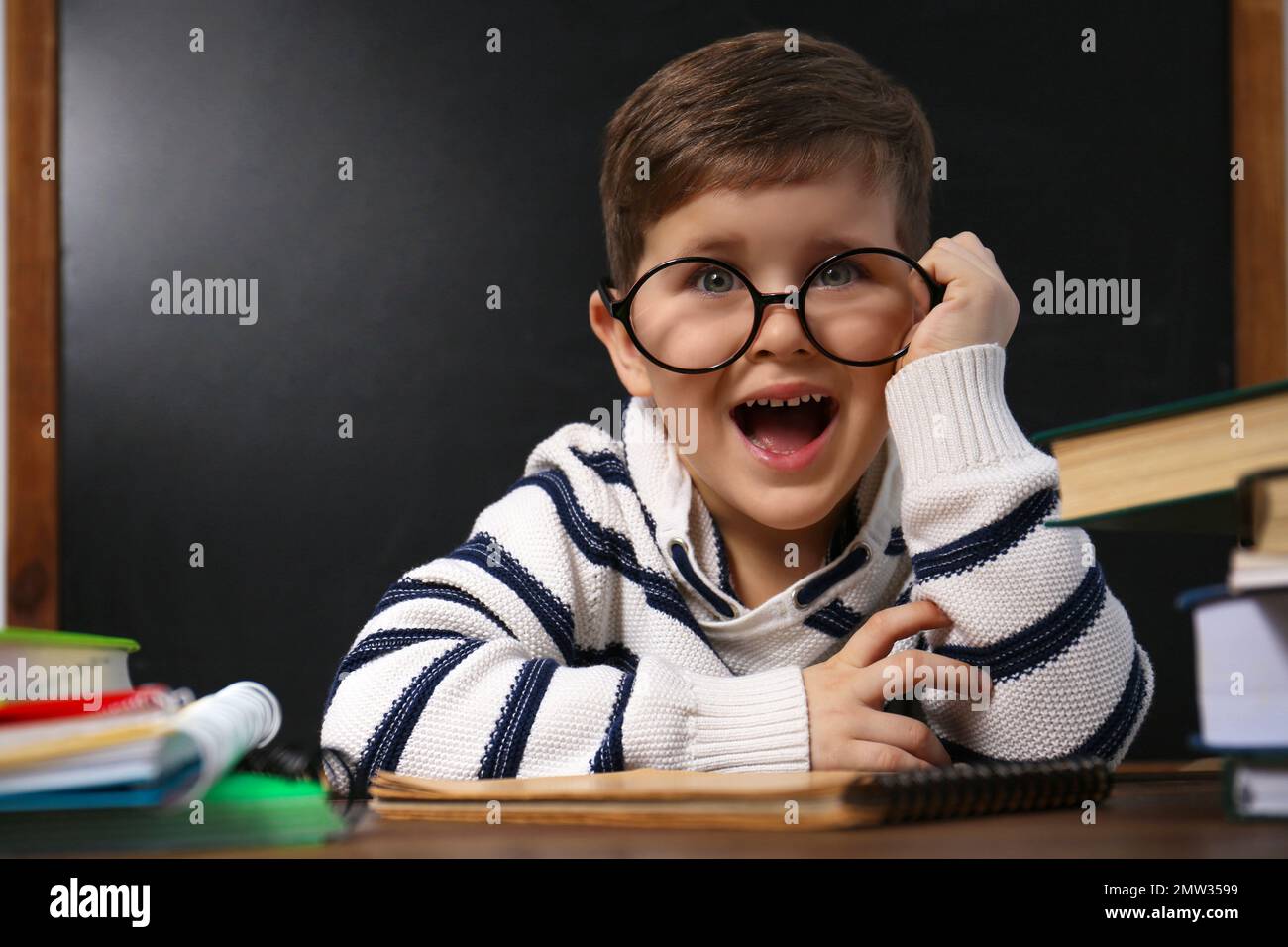 Cute little child wearing glasses at desk in classroom. First time at ...