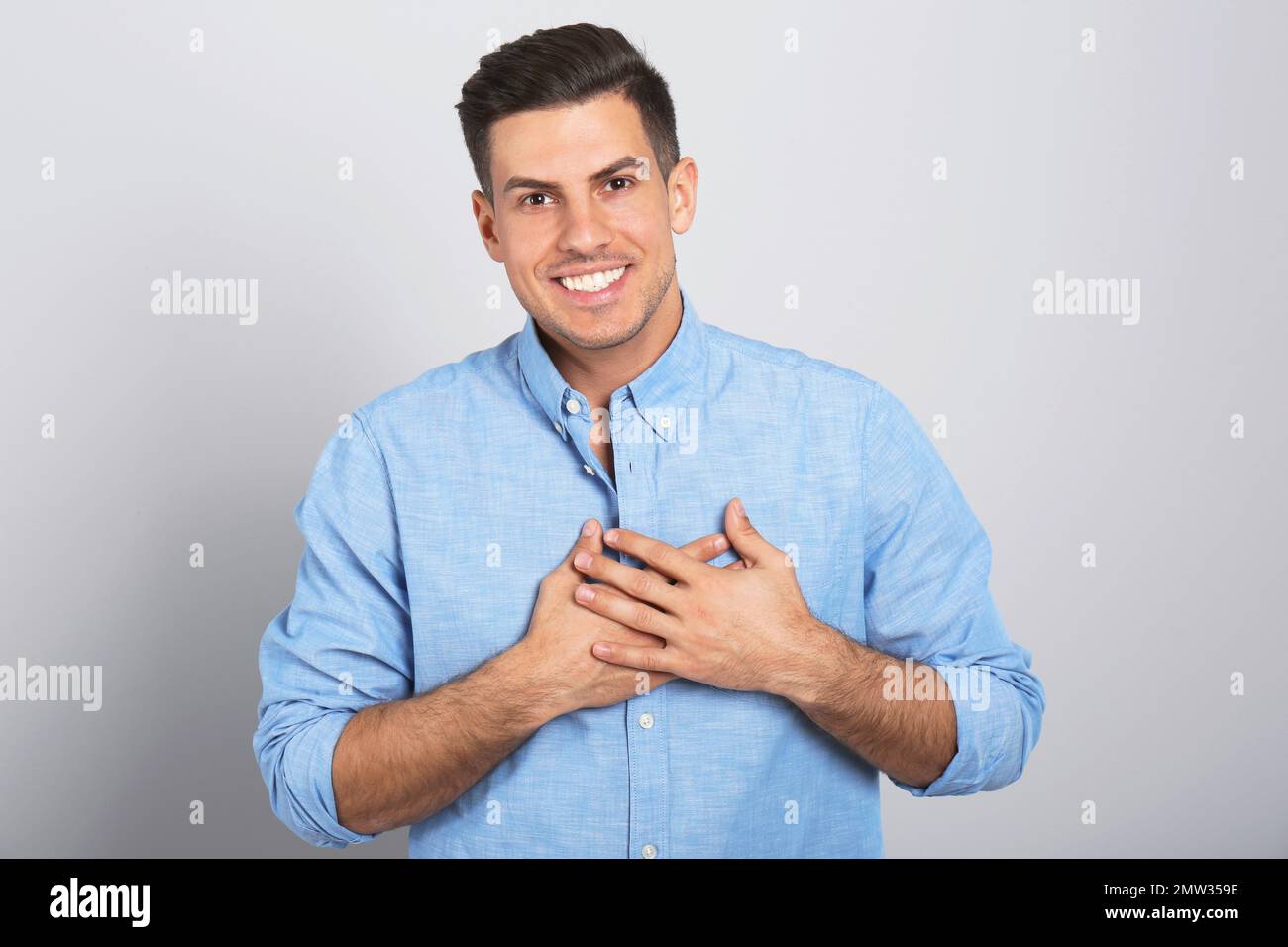 Handsome grateful man with hands on chest against light grey background ...