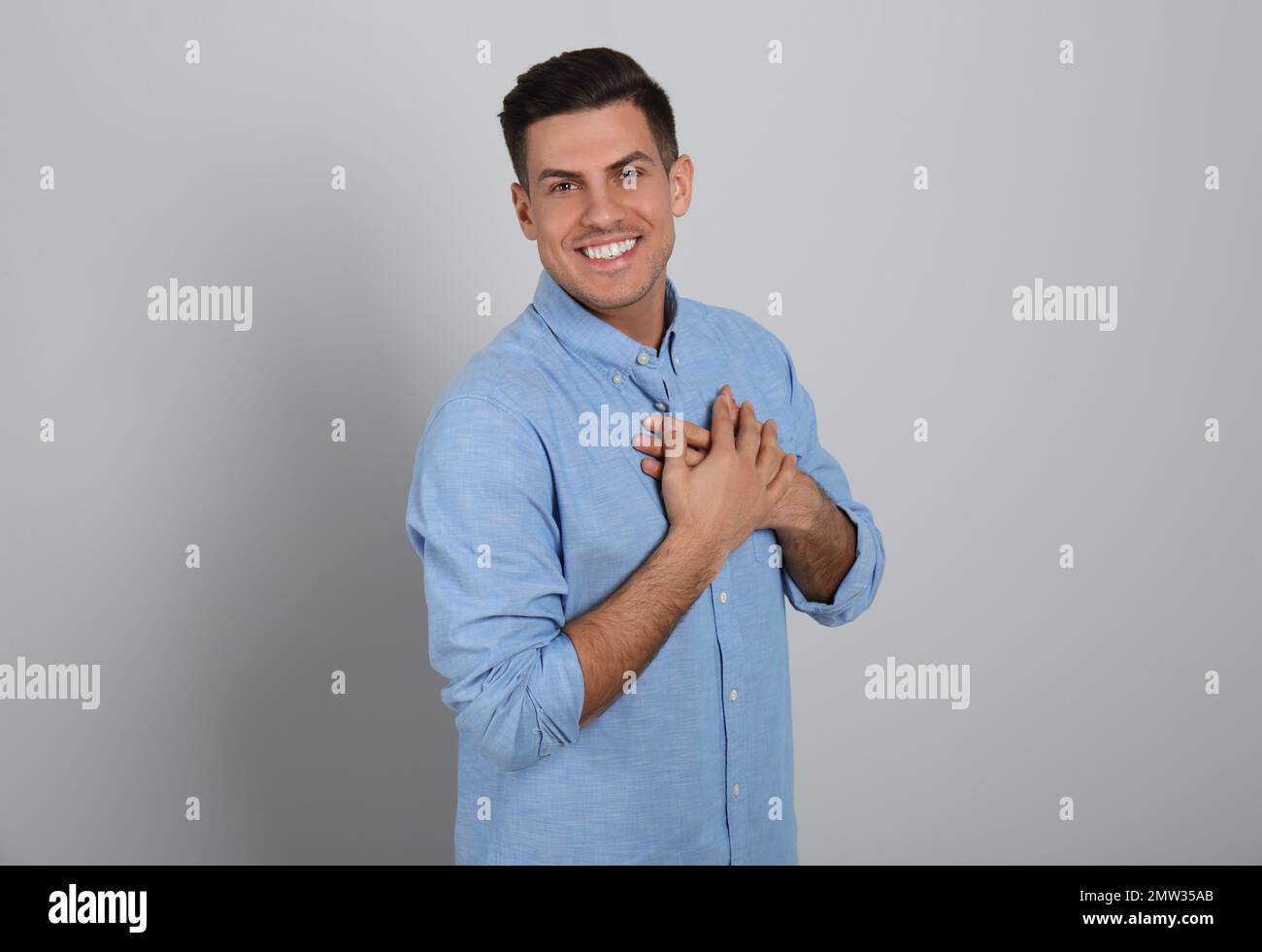 Handsome grateful man with hands on chest against light grey background ...