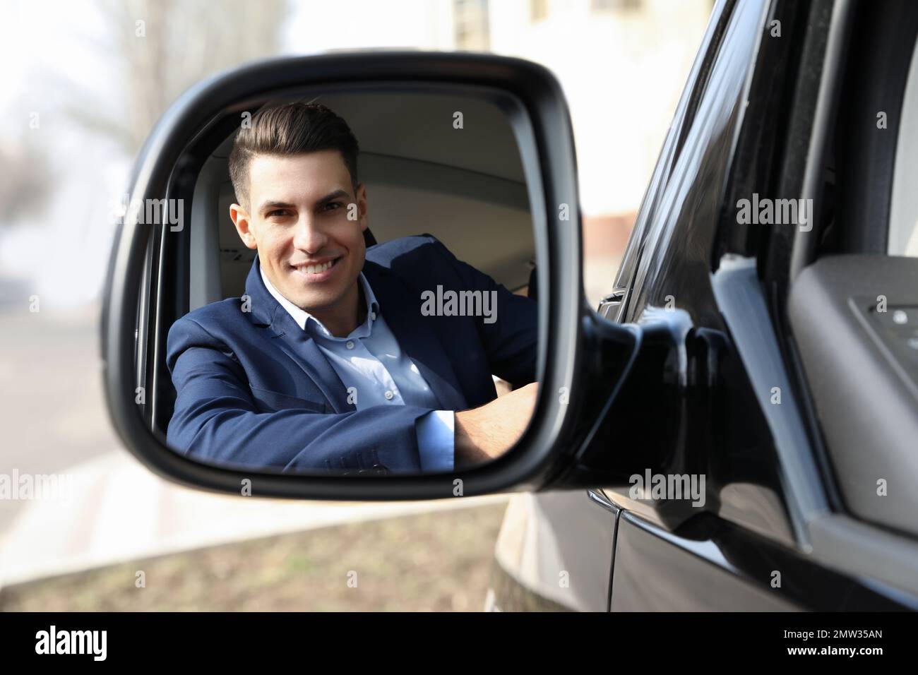 Handsome man looking into side view mirror of modern car outdoors Stock ...