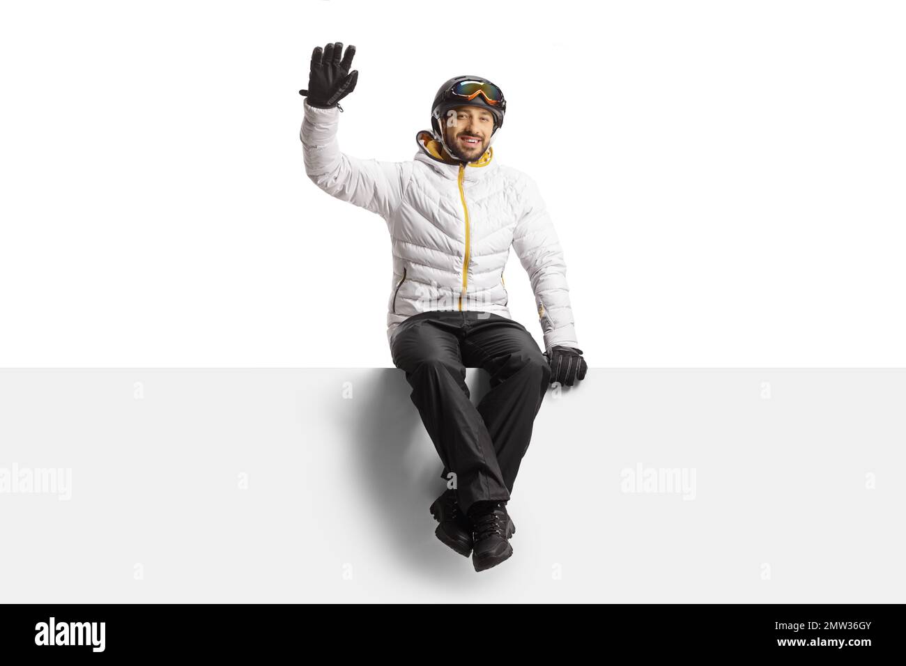 Young man wearing a skiing equipment sitting on a blank panel and ...