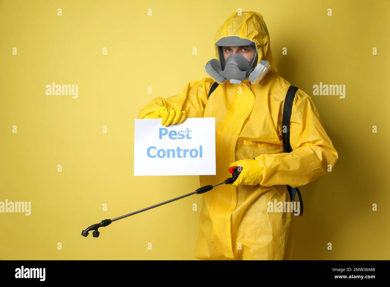 Man wearing protective suit with insecticide sprayer holding sign PEST ...