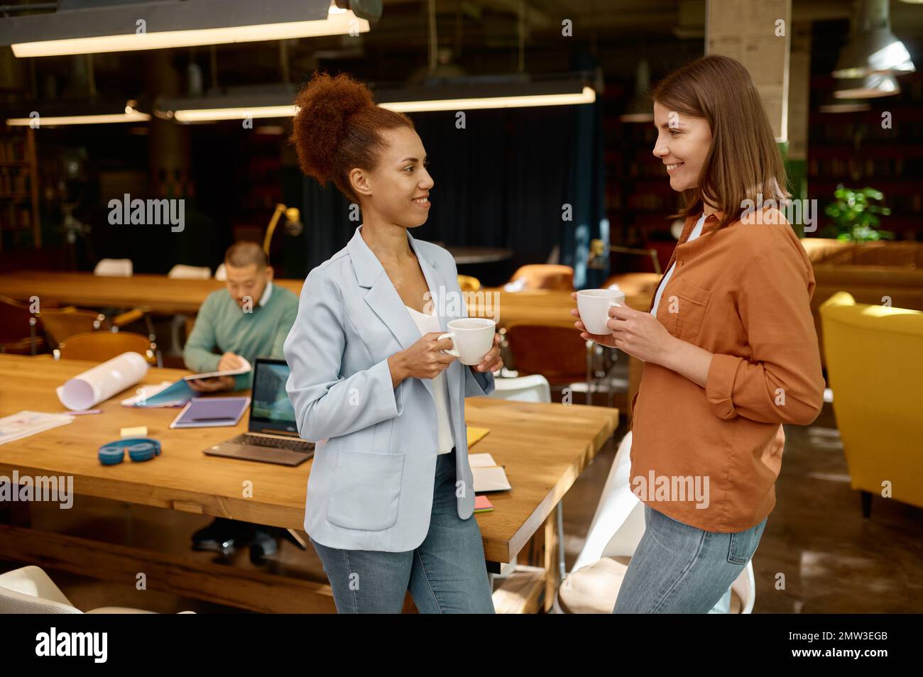 Two female coworkers talking during coffee break at coworking space ...