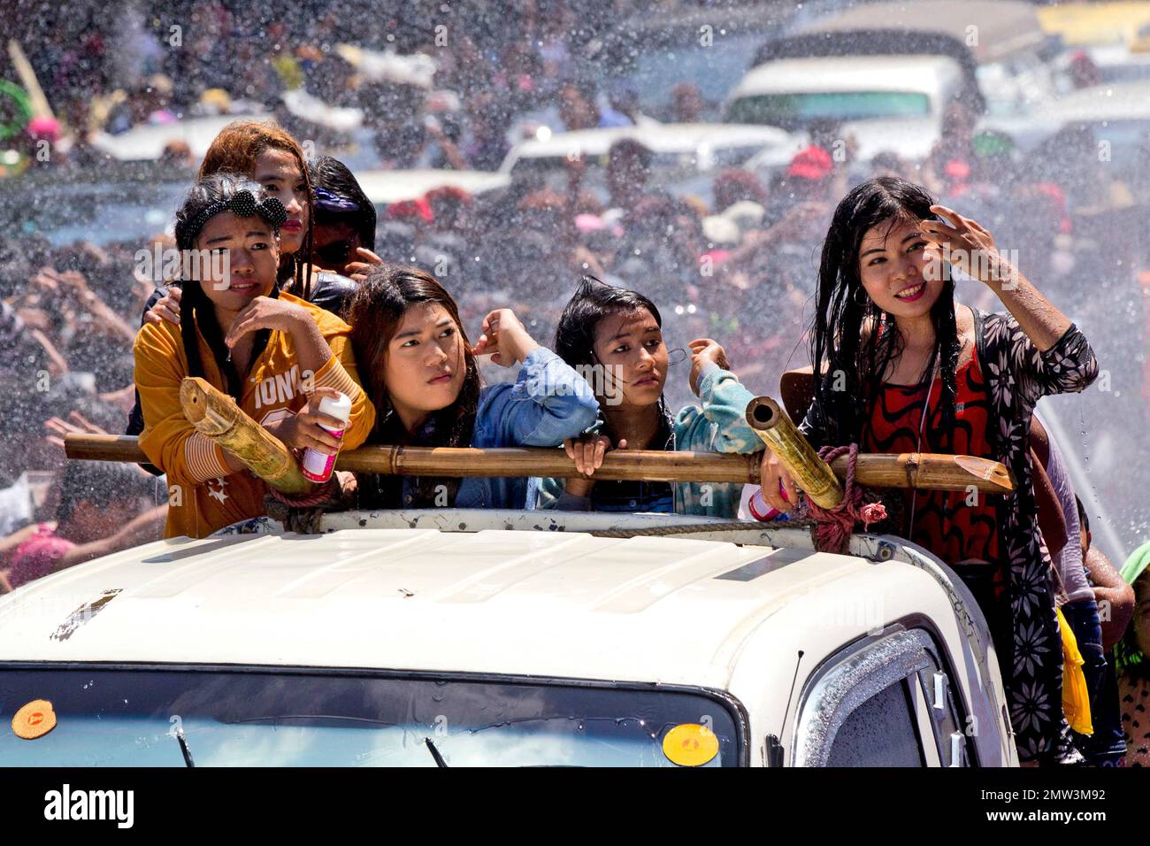 Revelers are sprayed with water as they ride in the back of a truck ...