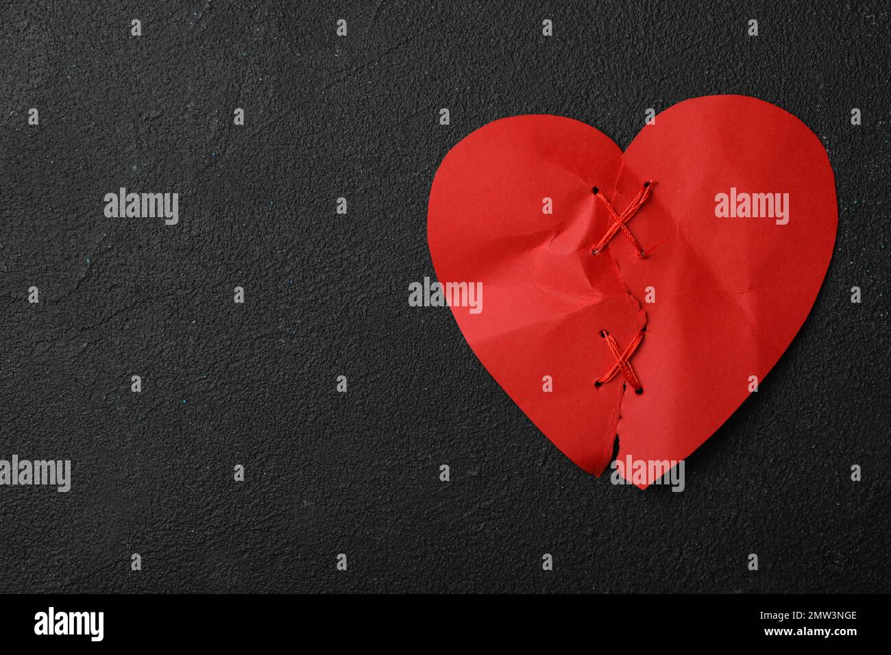 Top view of torn paper heart sewed with thread on black stone ...