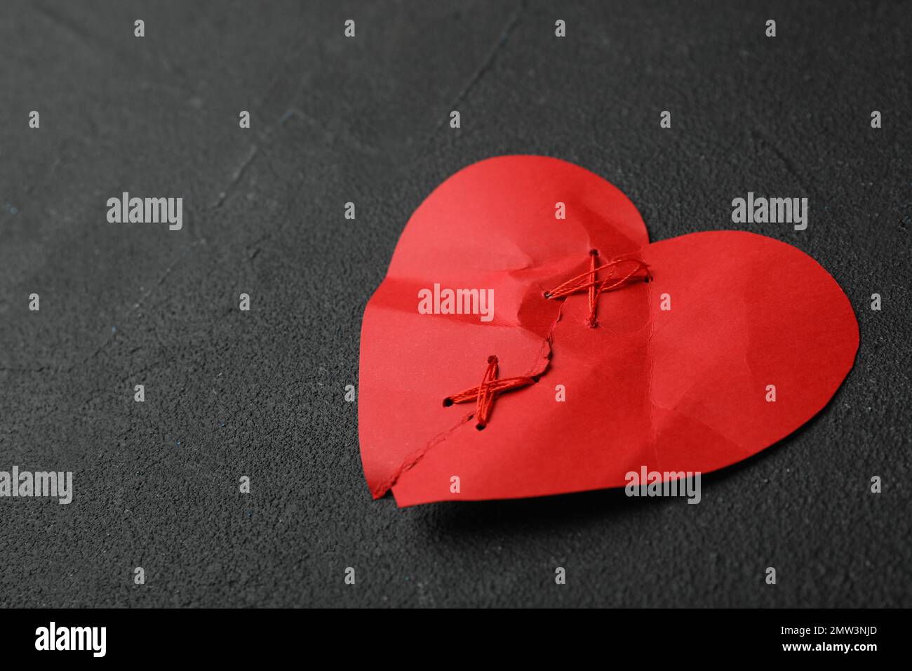 Torn paper heart sewed with thread on black stone background ...