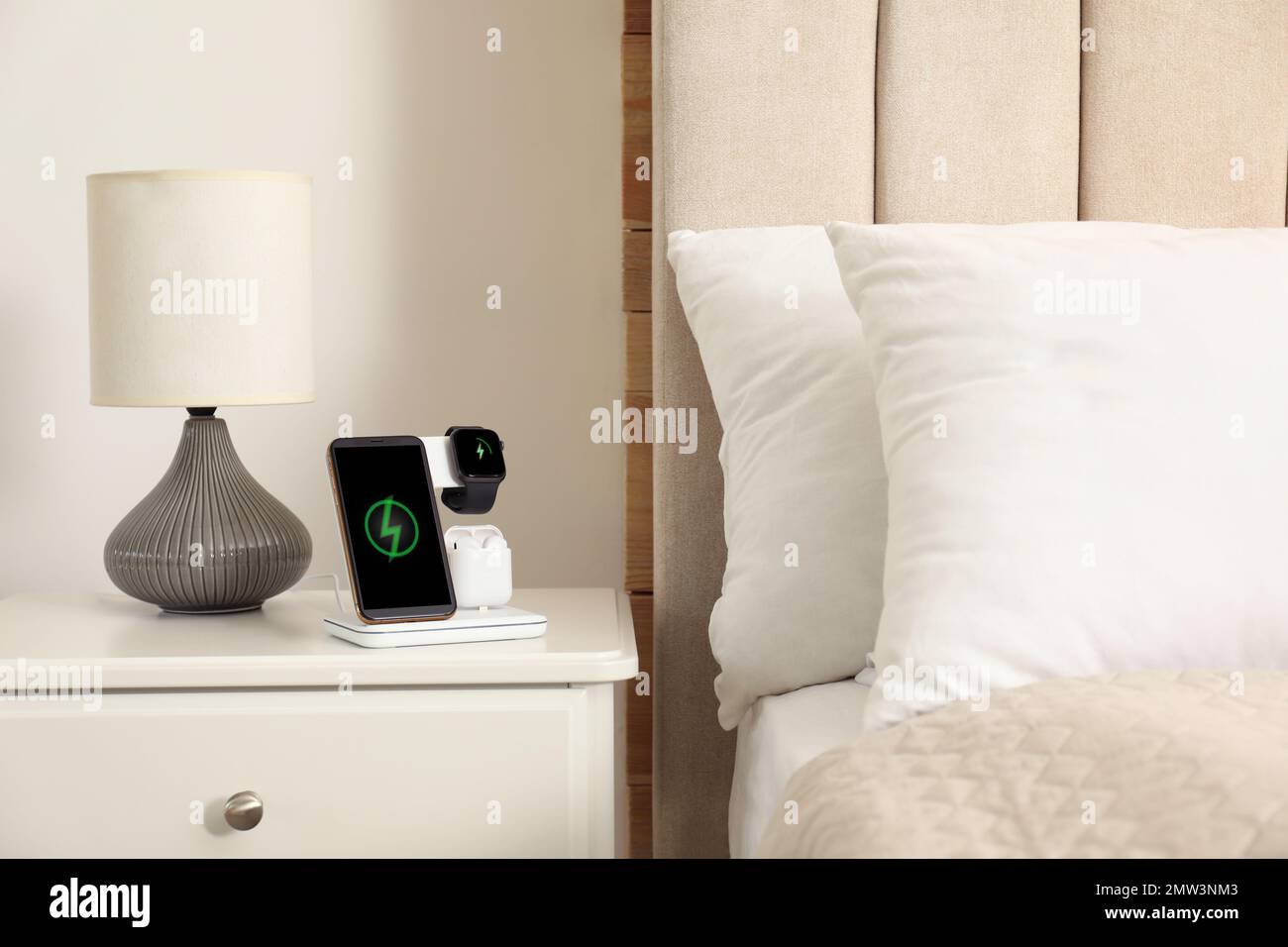 Different gadgets charging on wireless pad in bedroom Stock Photo - Alamy