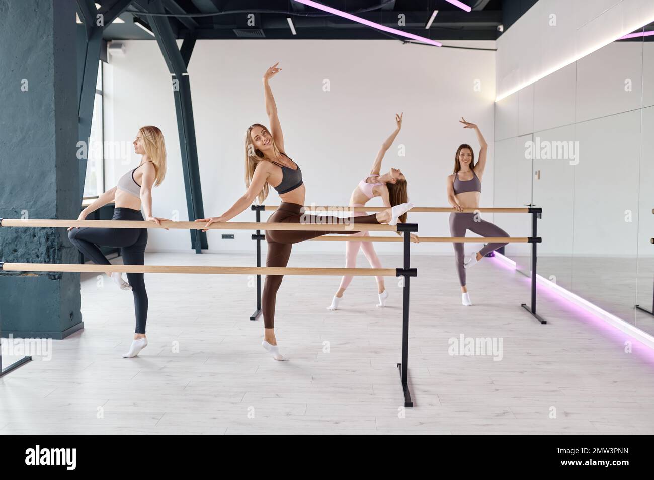 Young women dancers stretching legs, practicing ballet movement at ...