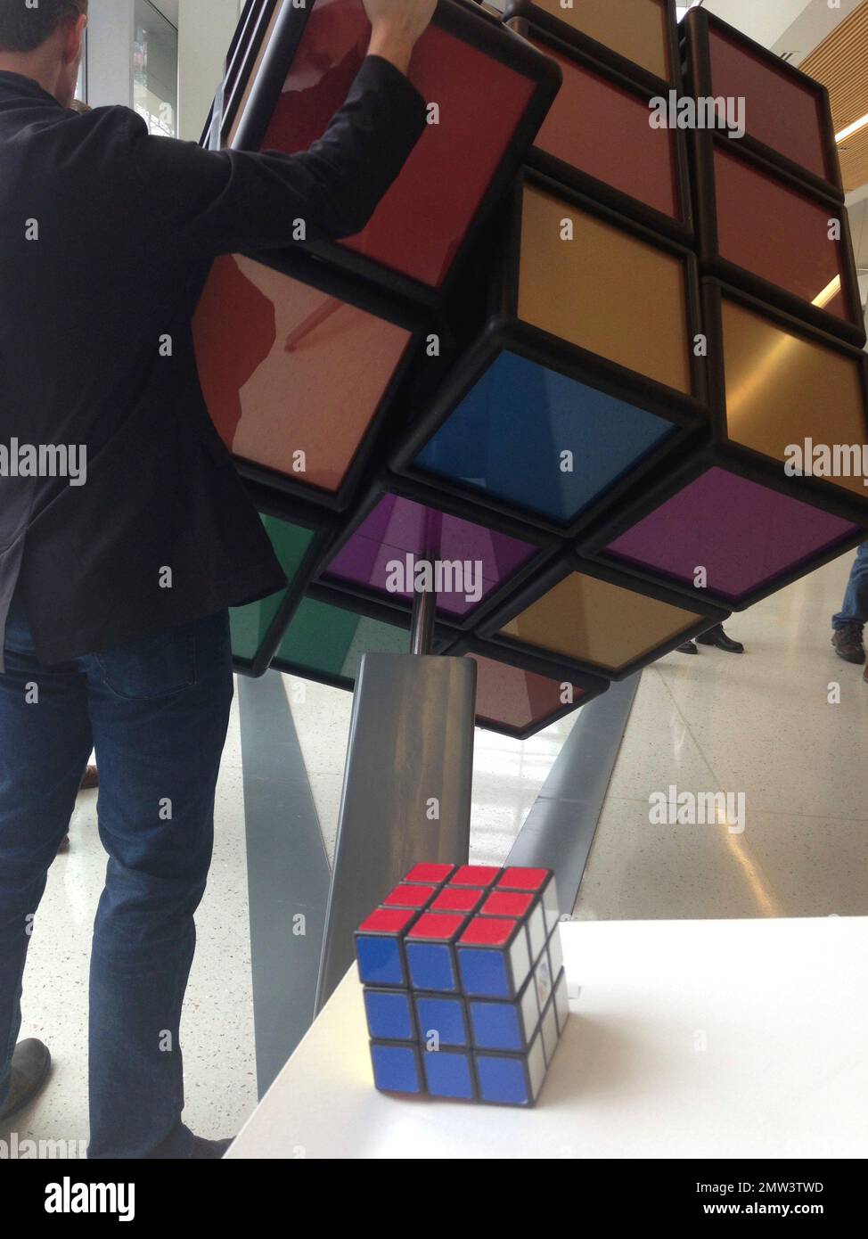 A traditional Rubik’s Cube sits on a podium in the foreground while a ...