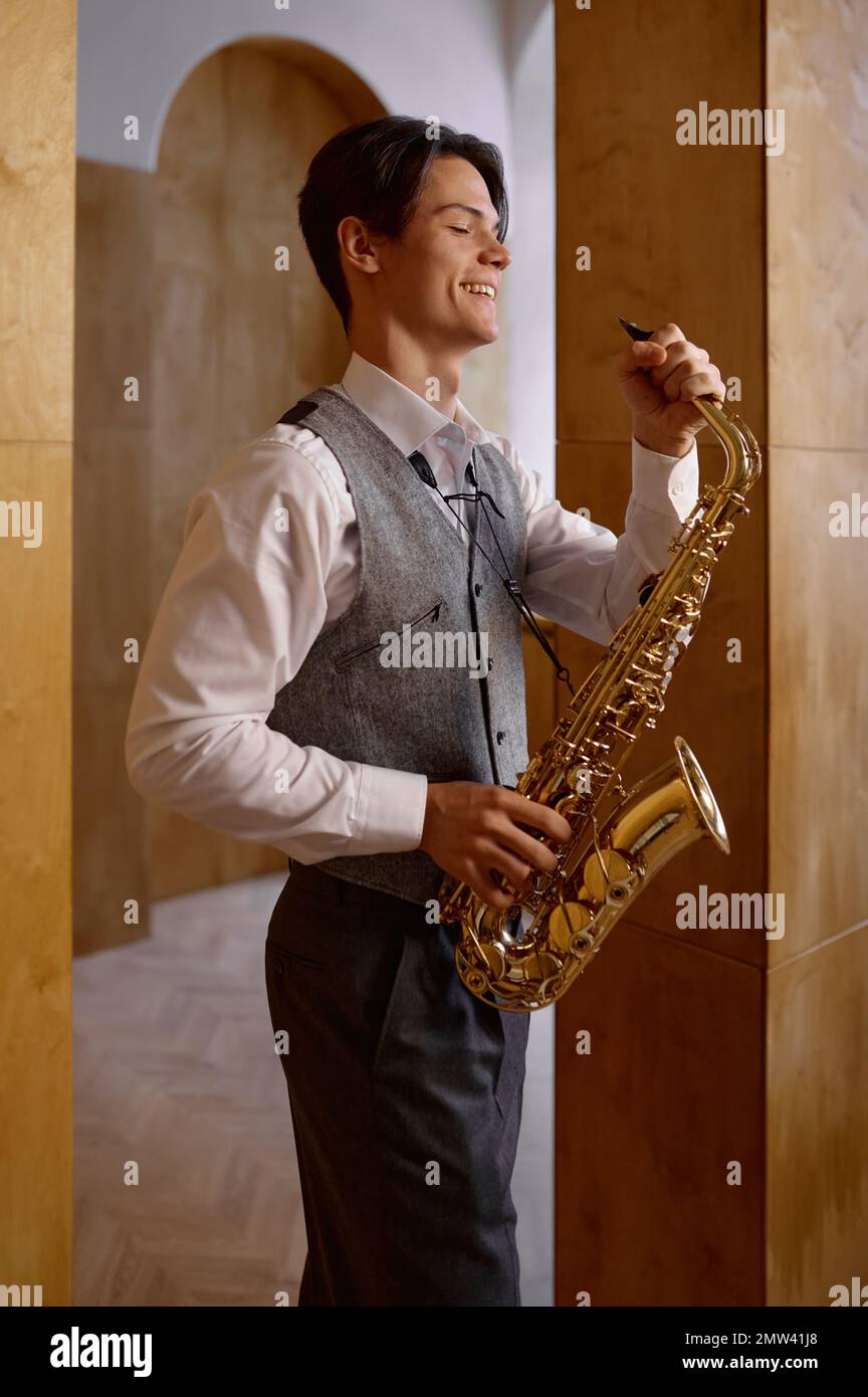 Jazz musician playing saxophone and leaning against art studio wall ...
