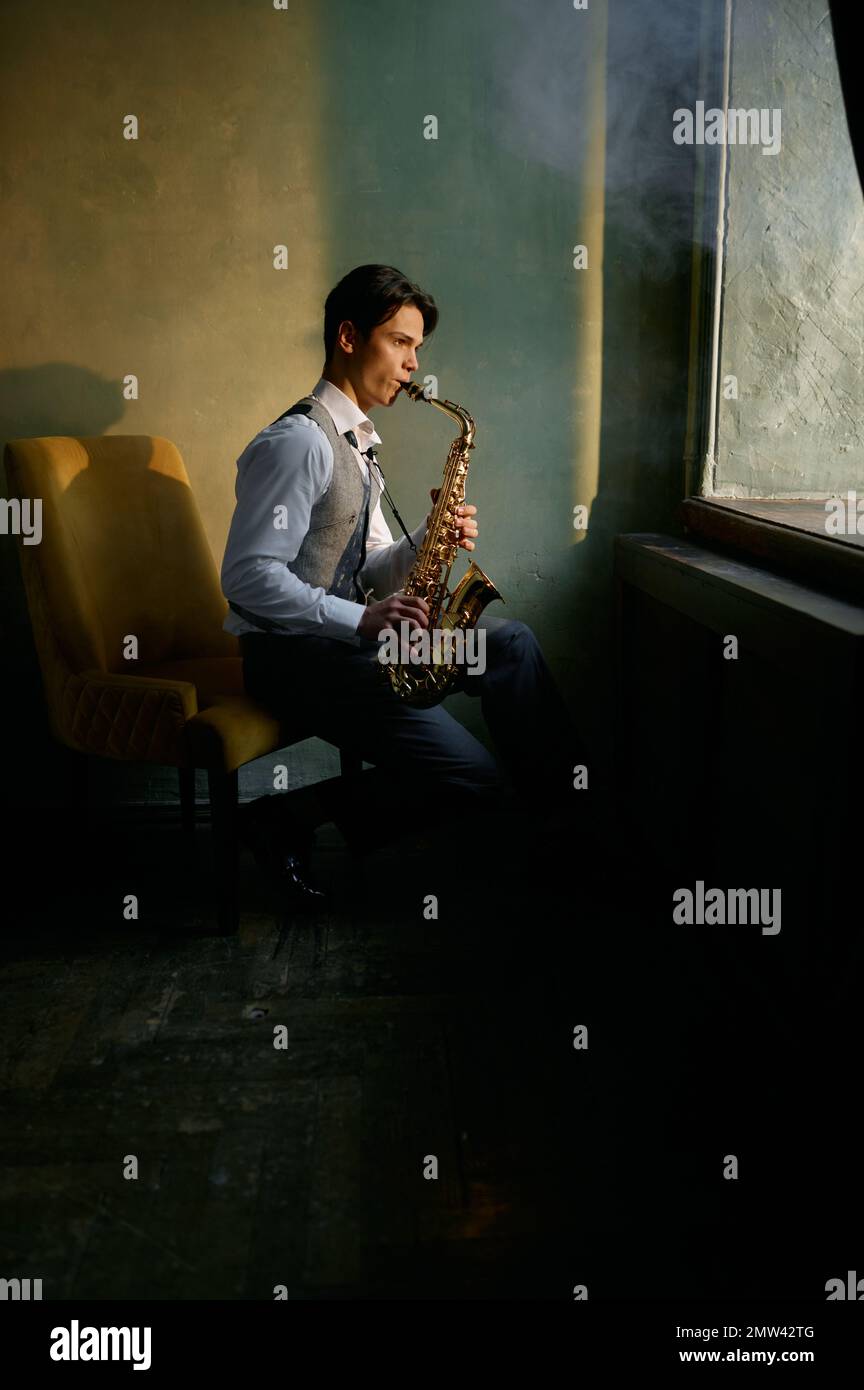 Jazz musician playing saxophone in front of window Stock Photo - Alamy