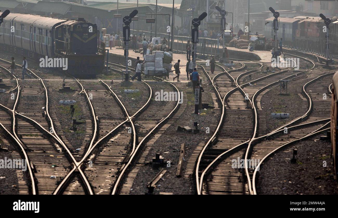 Indian laborers maneuver a cart fully loaded with goods across a ...