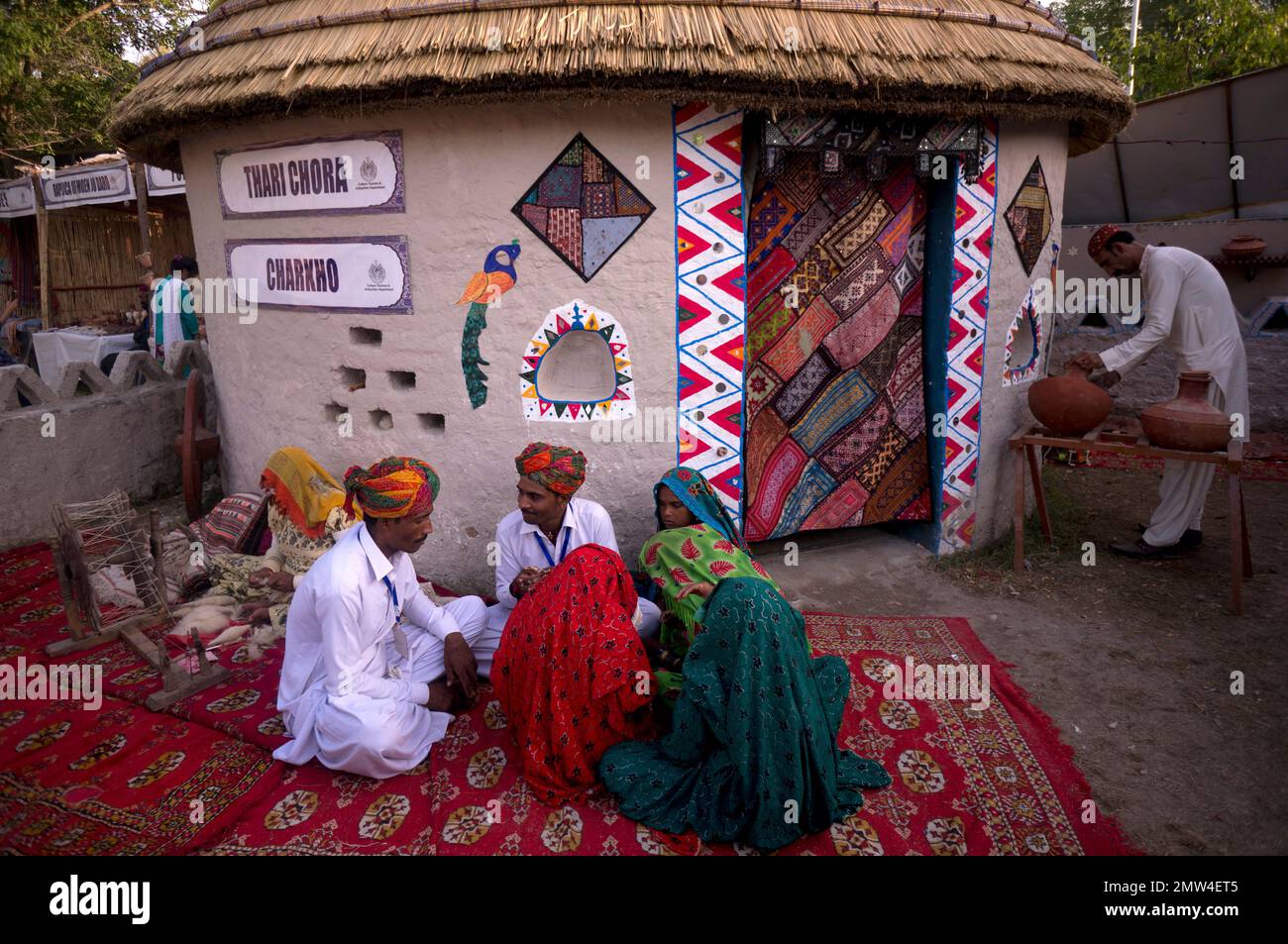 Pakistani folk artists sits outside a traditional hut at a folk ...