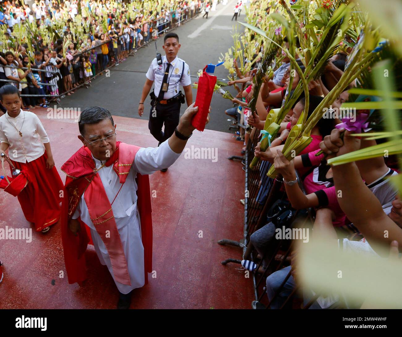 A Roman Catholic priest blesses with holy water devotees waving palm ...
