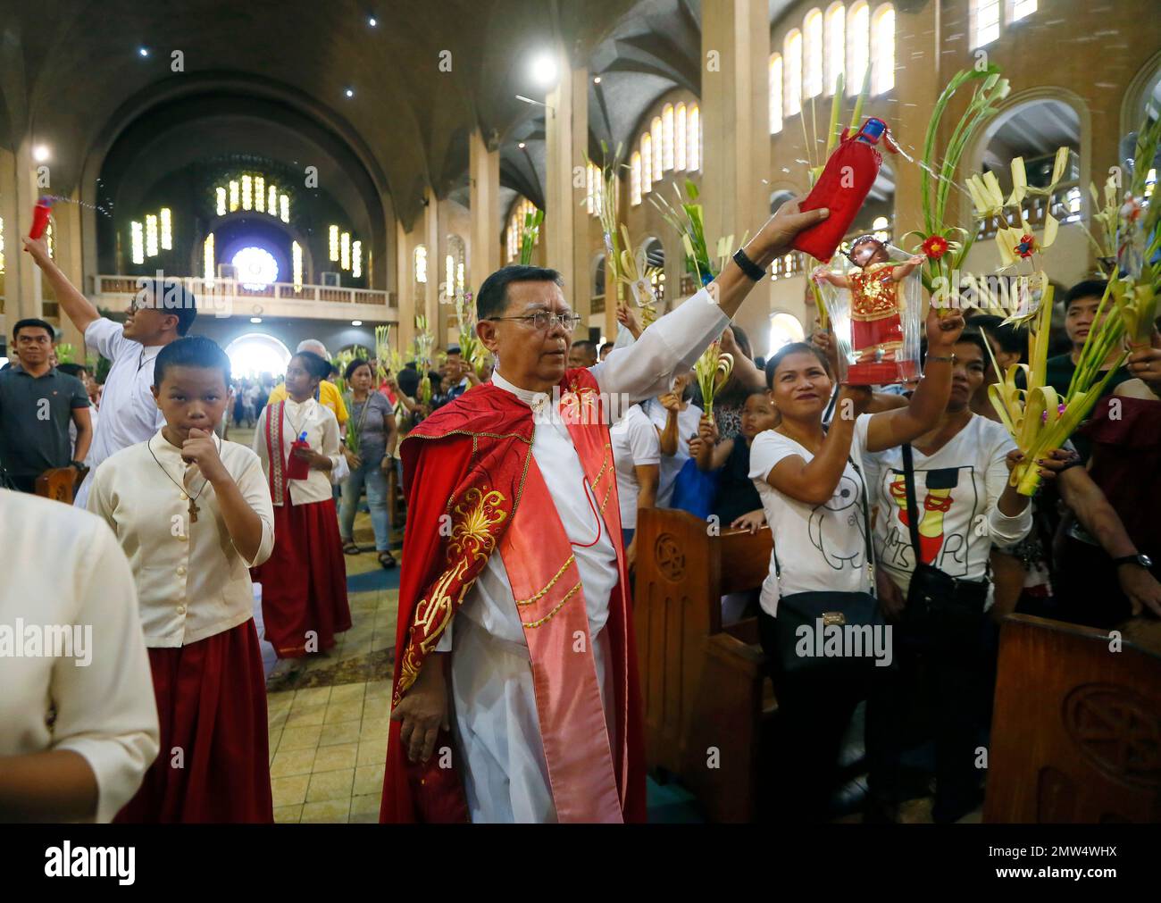 A Roman Catholic priest blesses with holy water devotees waving palm ...