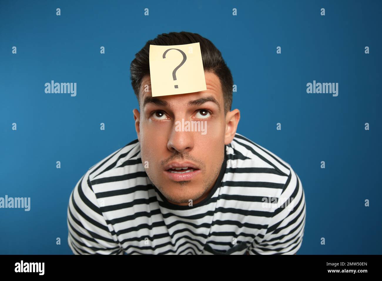 Emotional man with question mark sticker on forehead against blue ...