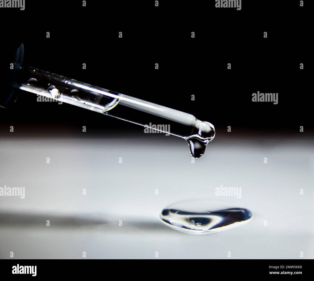 Liquid transparent gel drips from a serum pipette with drops on a light ...