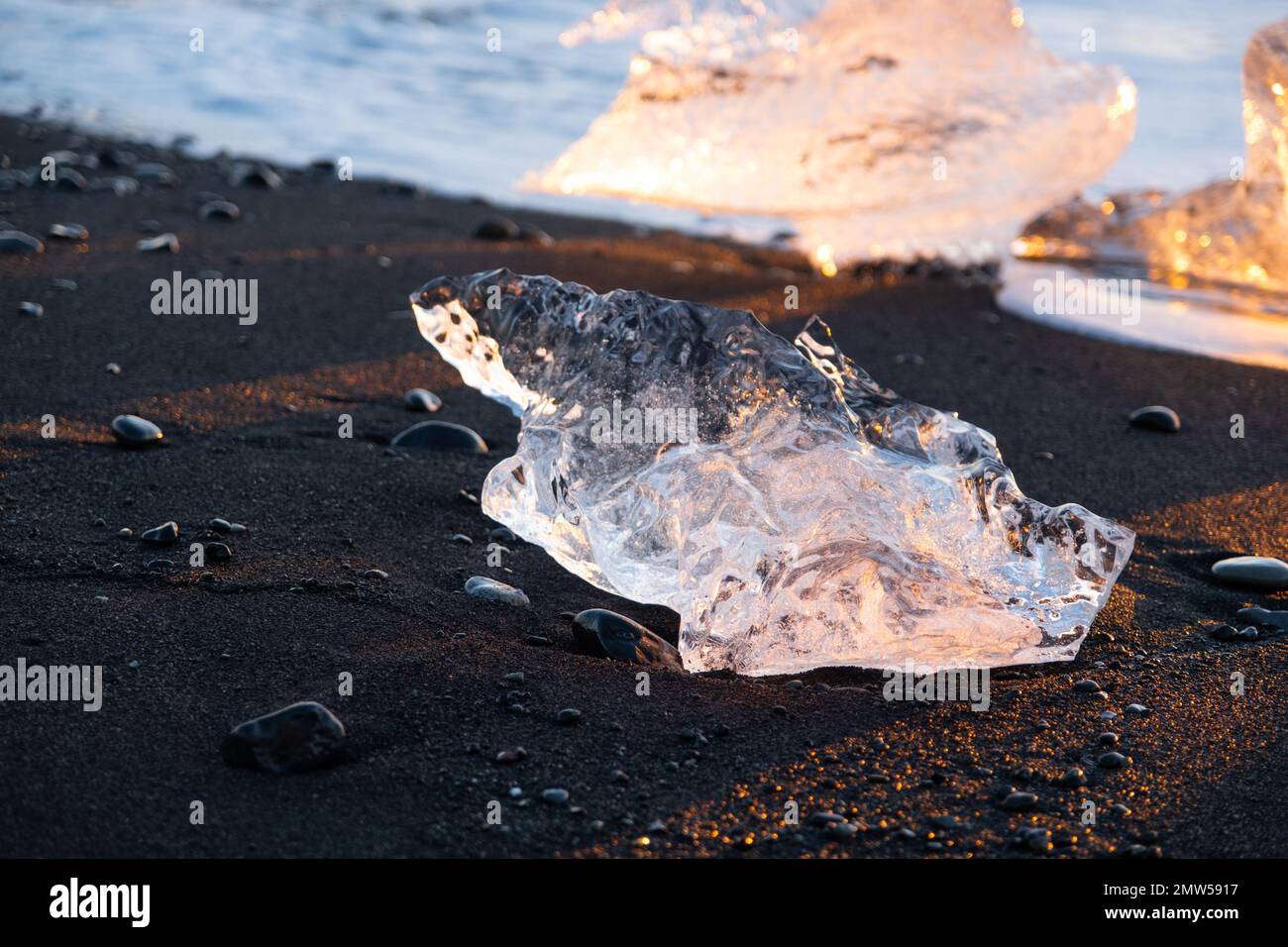 Pure Ice Shining on Black Volcanic Sand at Sunset, Ocean Waves Crash ...