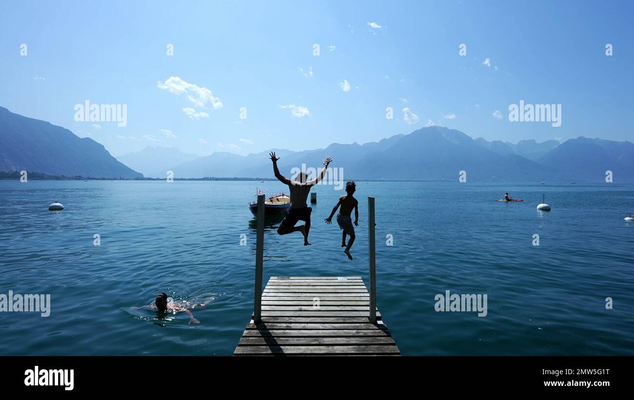People jumping into lake water. Father and son running in Swiss pier ...