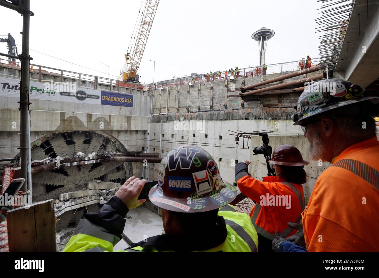 Workers look on and take photos as a massive tunneling machine breaks ...
