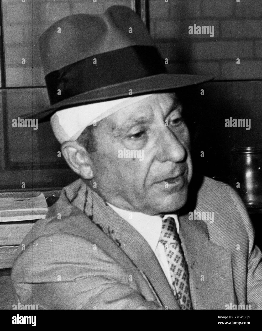 Gambler Frank Costello wears a hat over his bandaged head as he is ...