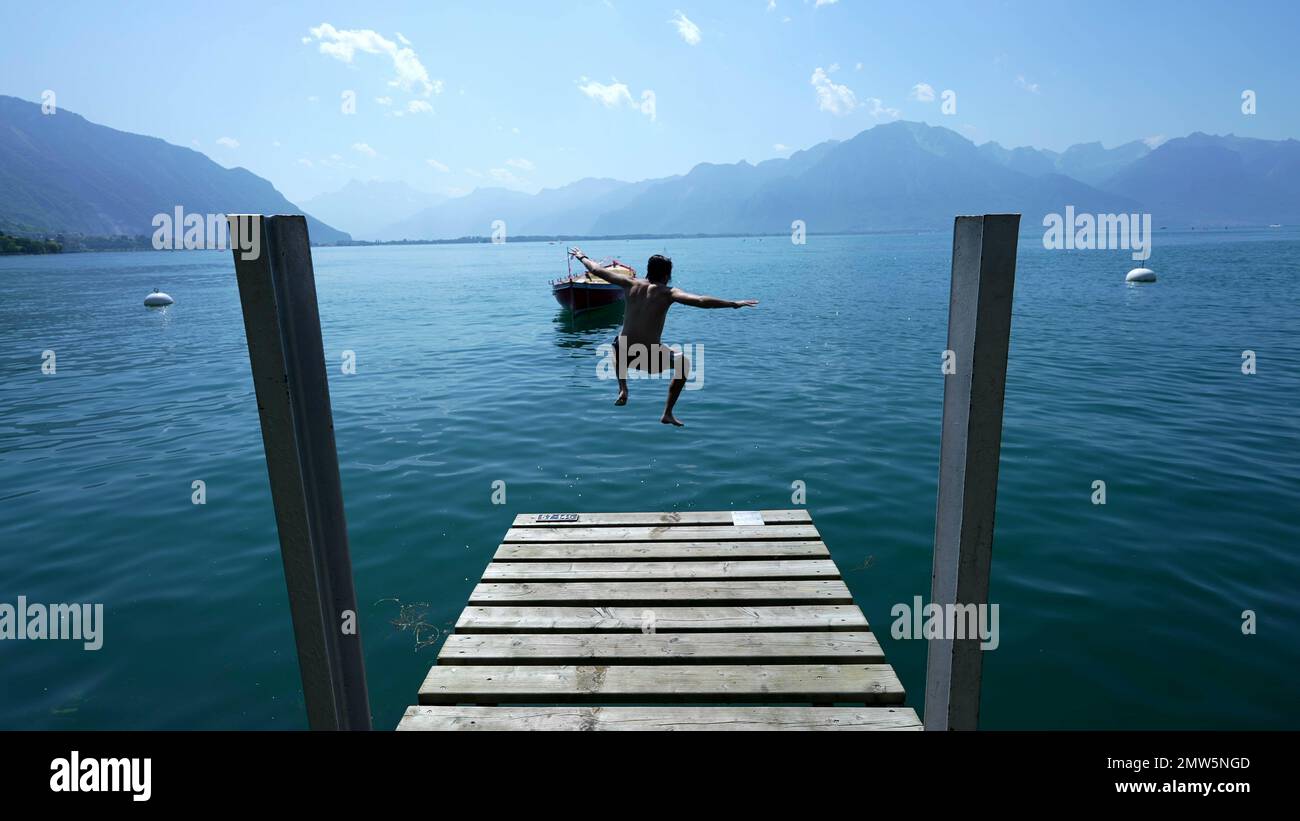 Person running at lake pier and jumping into water. Young man runs in ...
