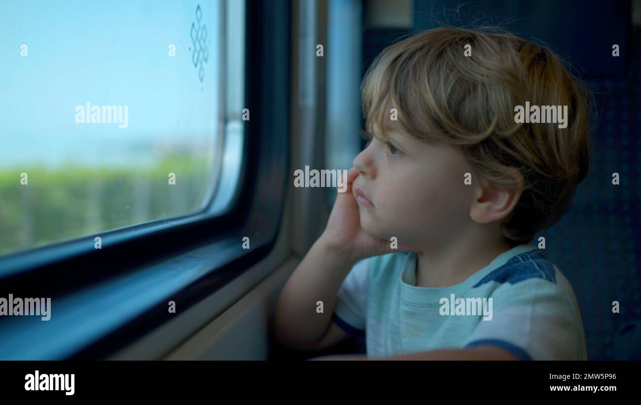 Small child leaning on train window staring at landscape passing by ...