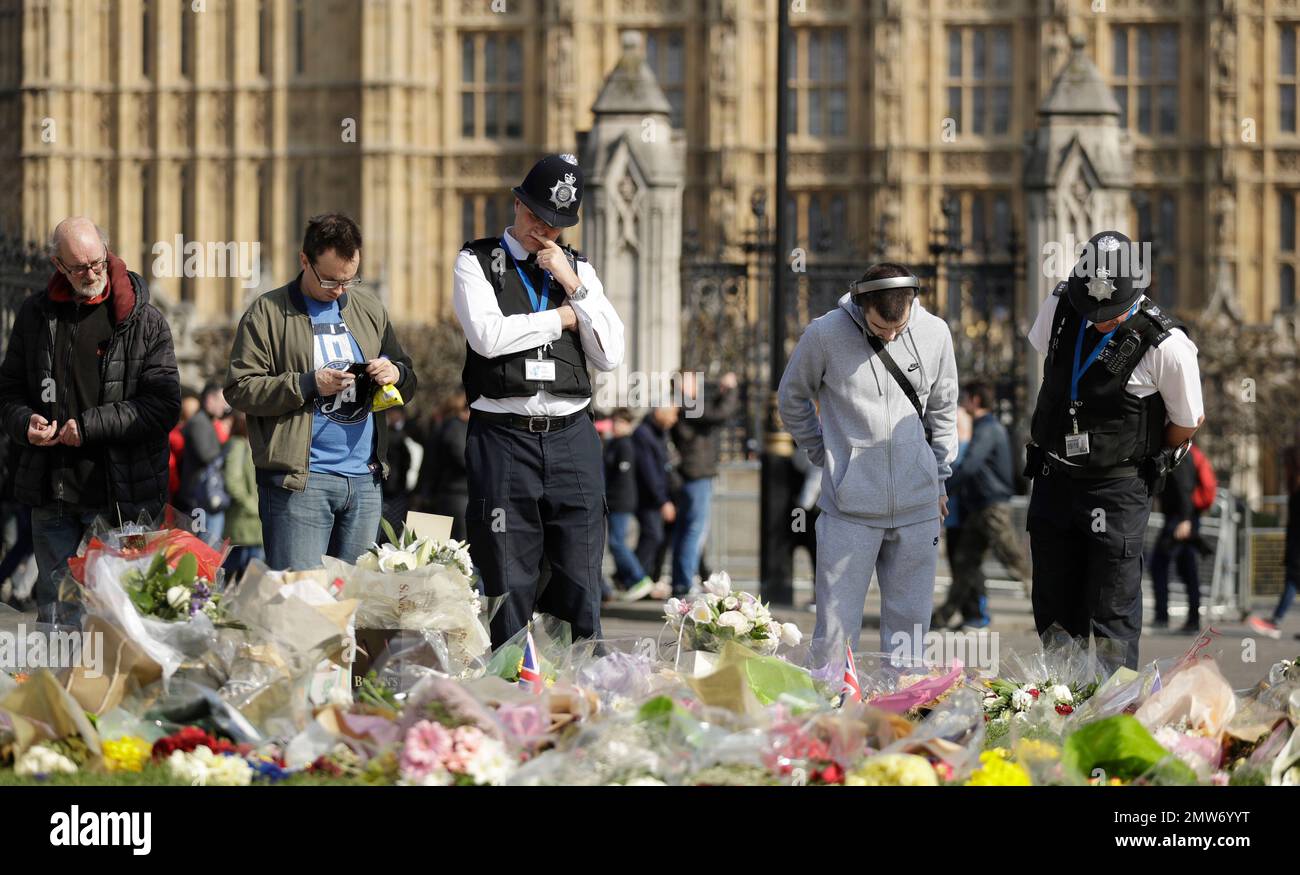 Police officers and members of the public look at the floral tributes ...