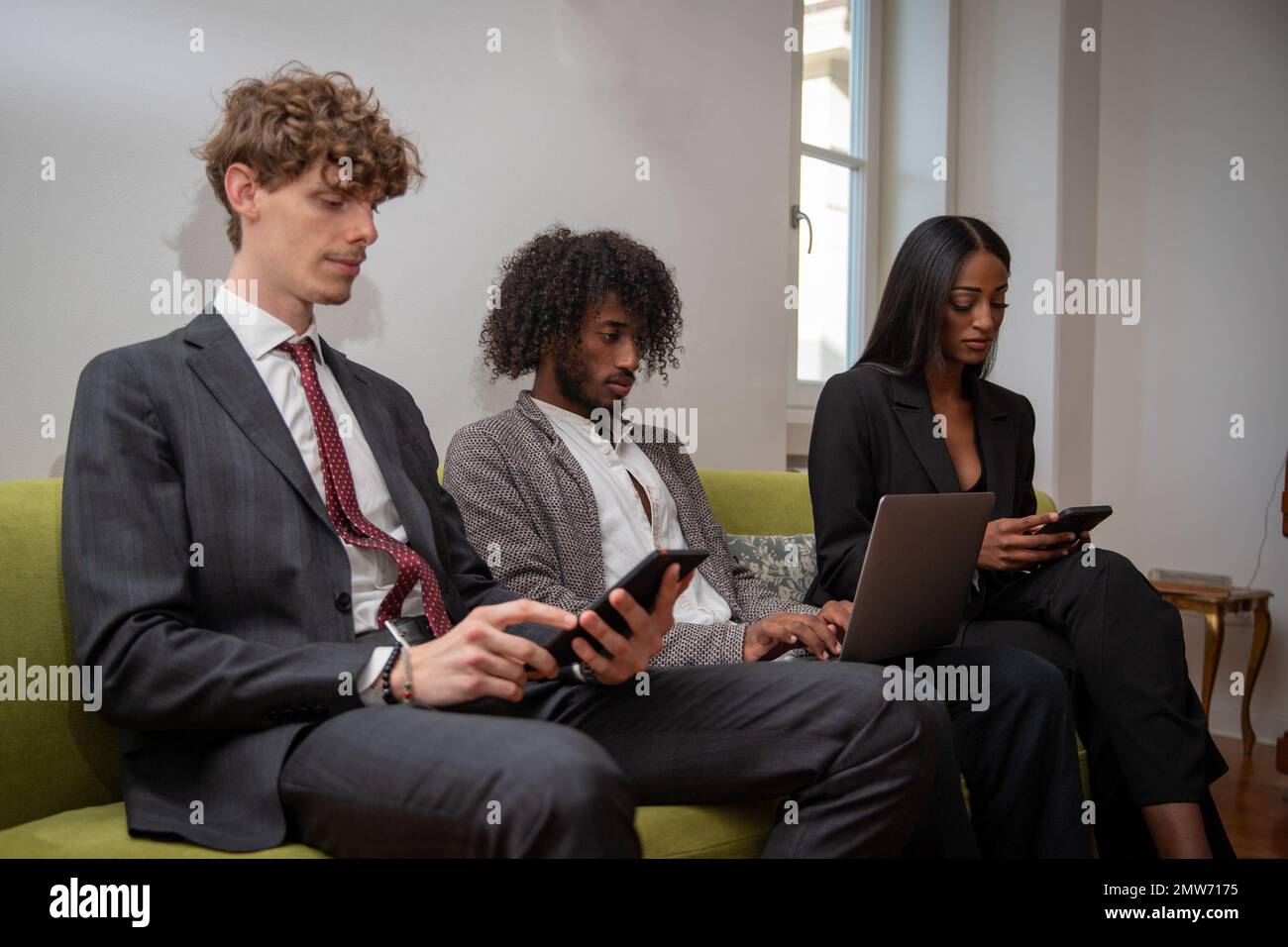 Three colleagues use their tech devices while sitting on the sofa at ...